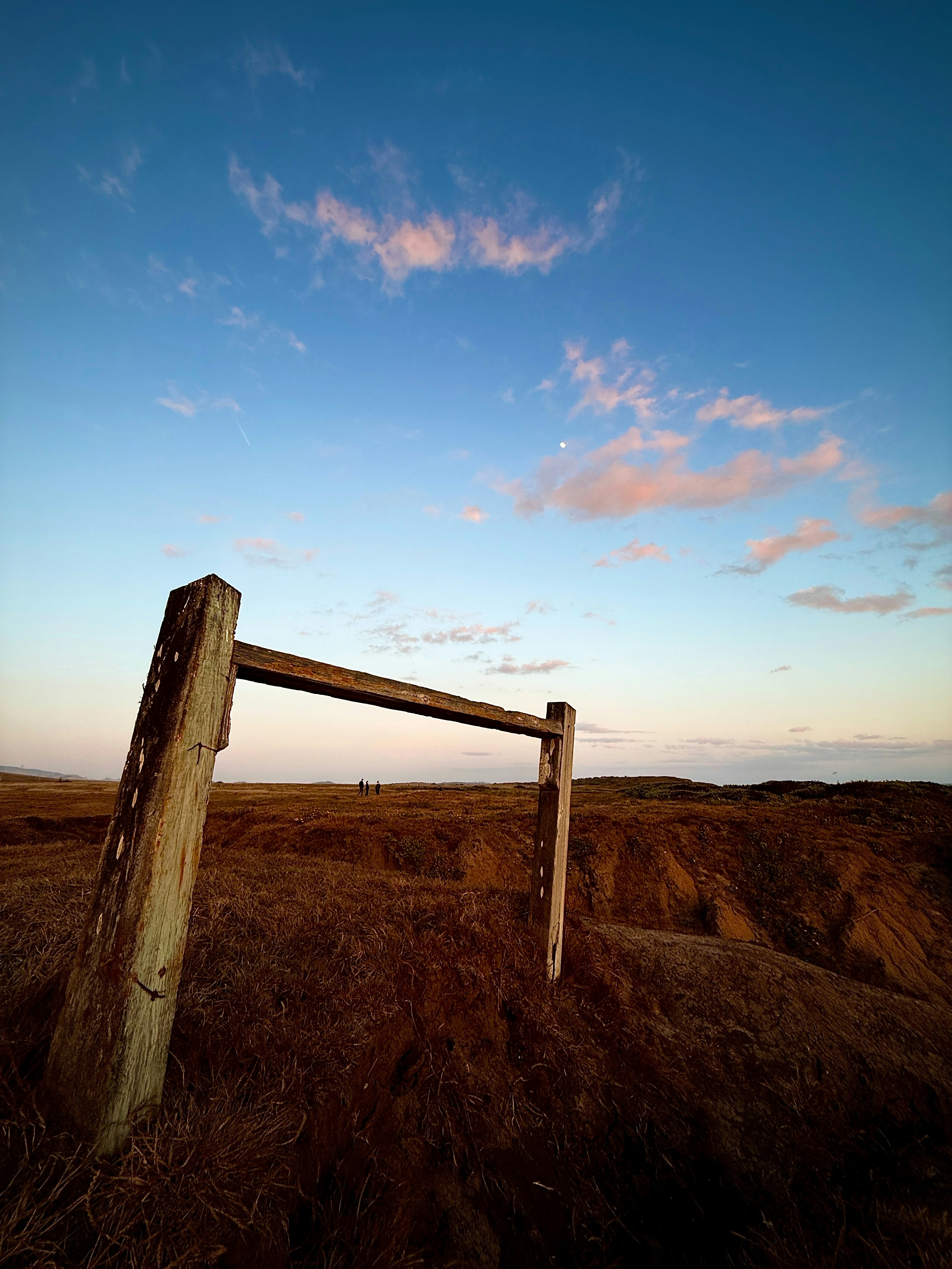 Old wooden fence post in dry landscape under blue sky.