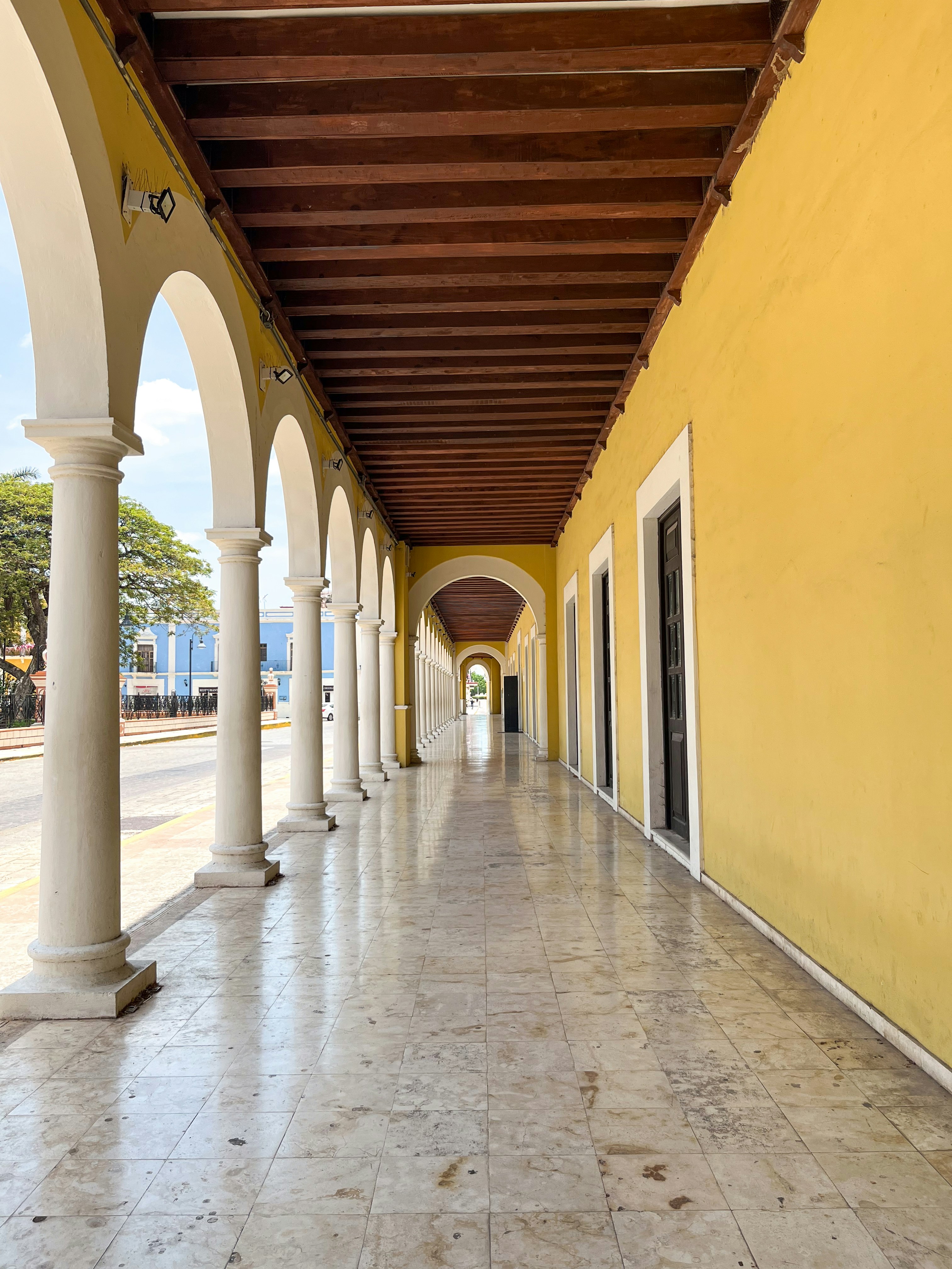 Arched hallway with white columns, yellow wall, and wooden ceiling ...