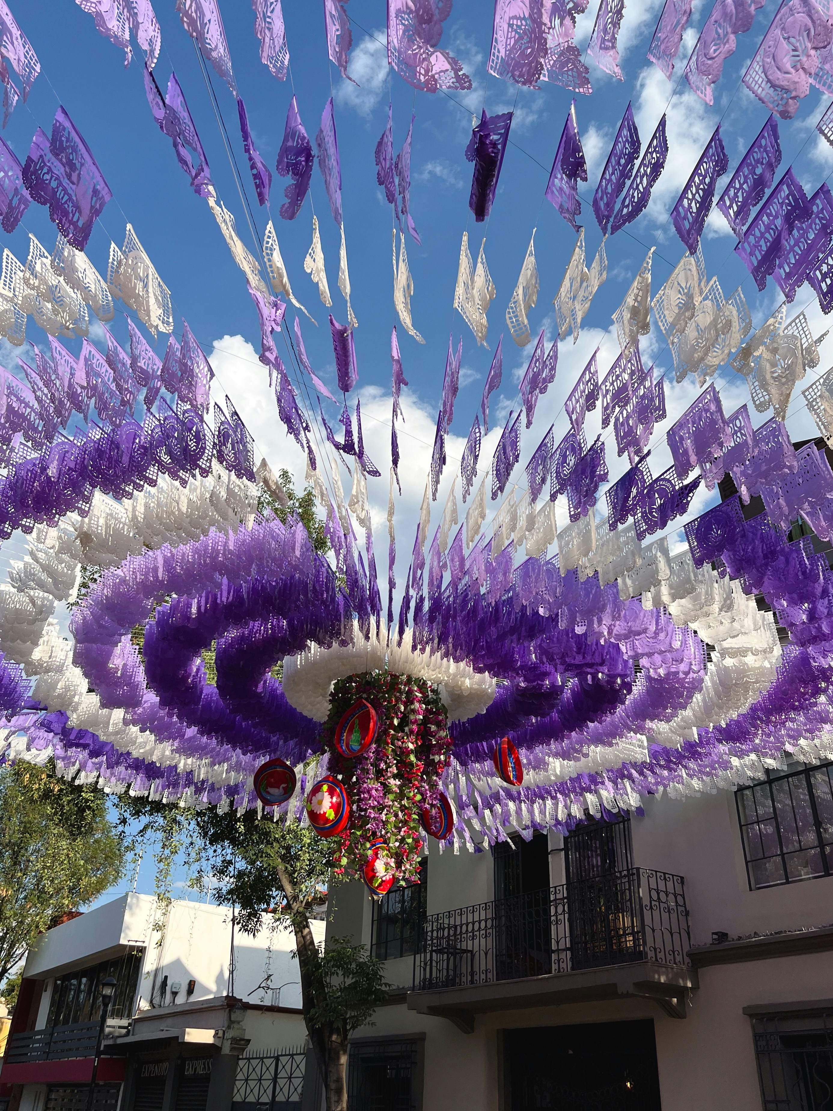 Vortex of Color: Hanging Flags Circling a Floral Center Above a Sunlit Street