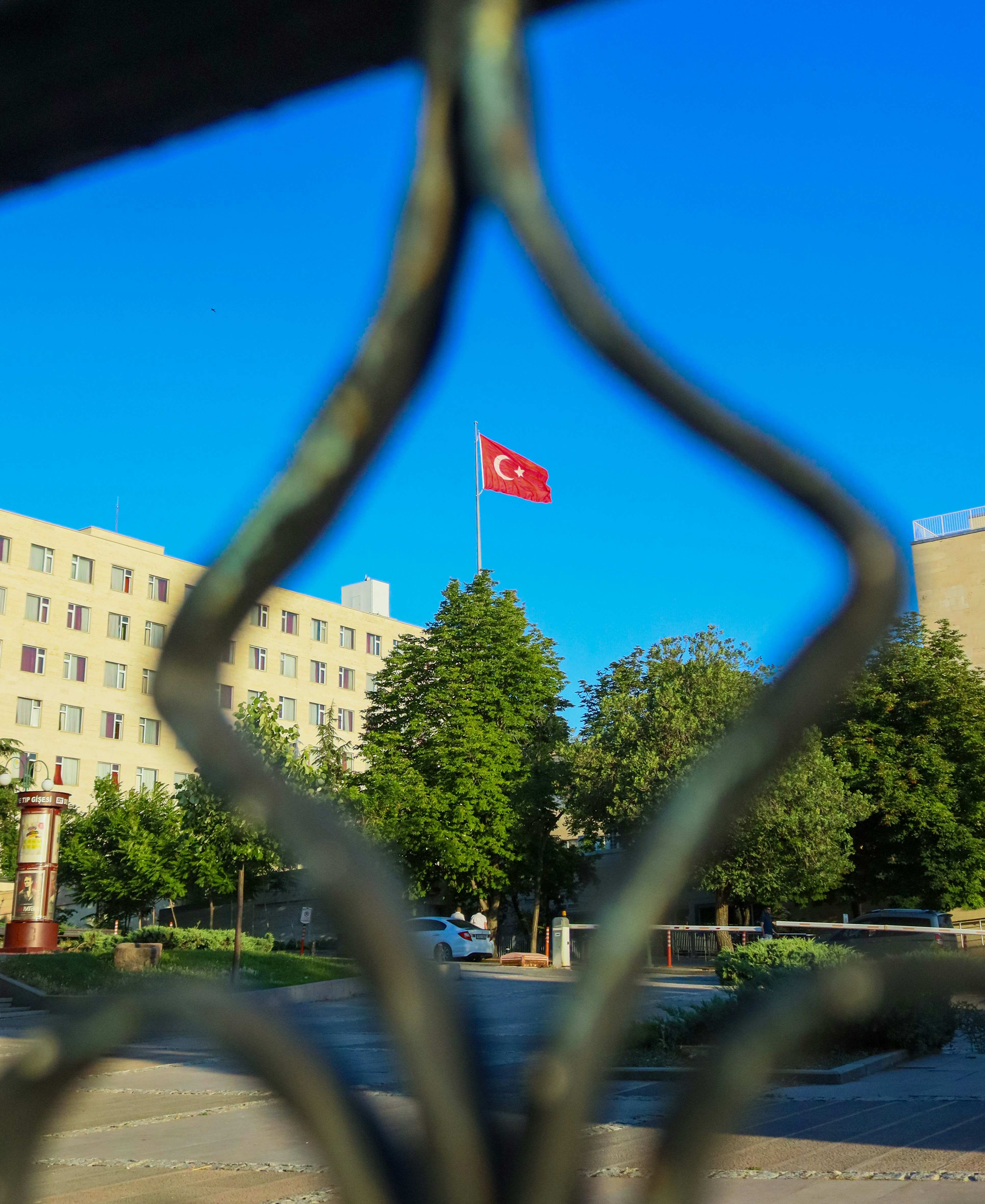 Turkish Flag Rising Above Cityscape Framed by Wavy Fence
