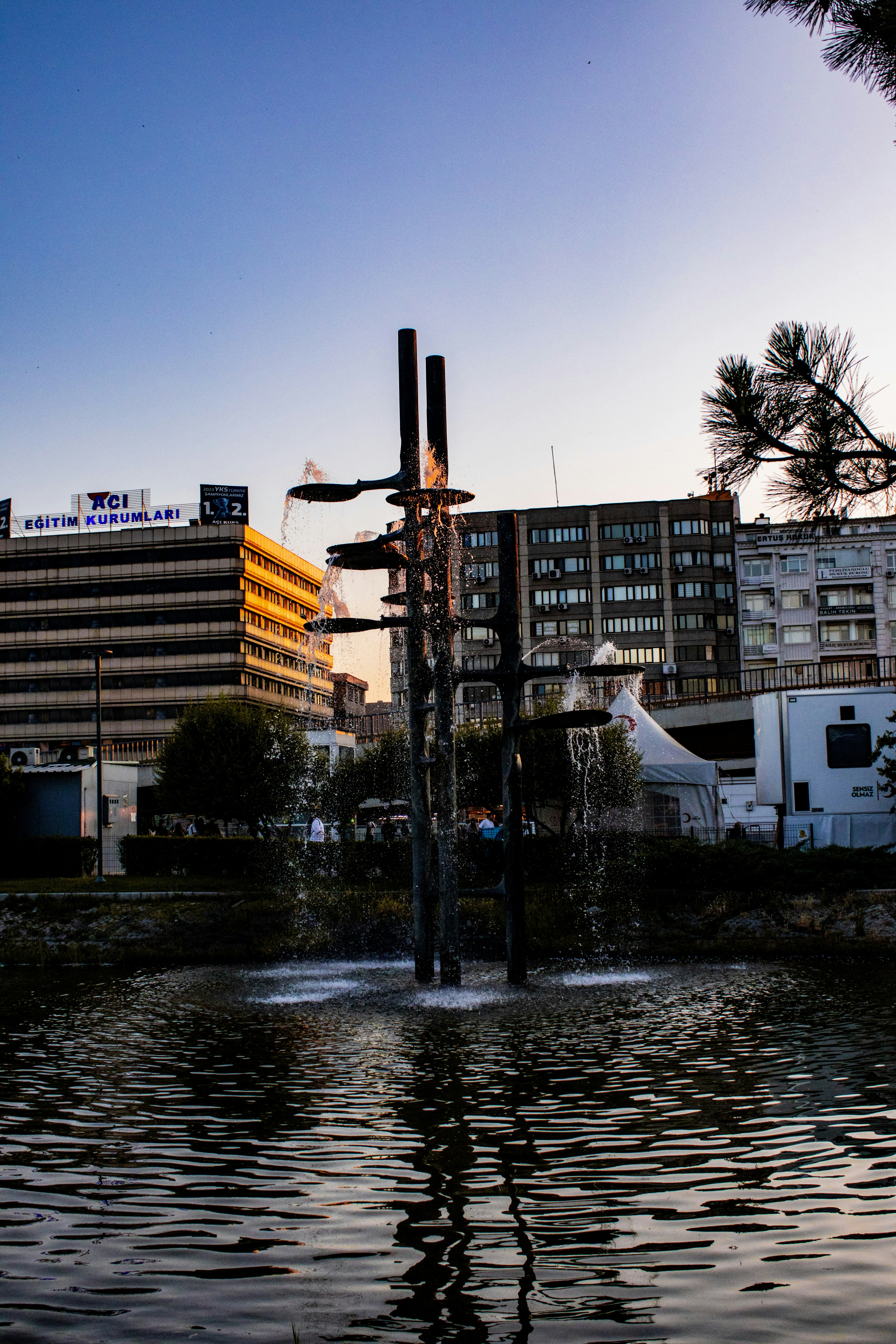 Urban Fountain at Dusk: A Tapered Water Sculpture Amidst City Glow