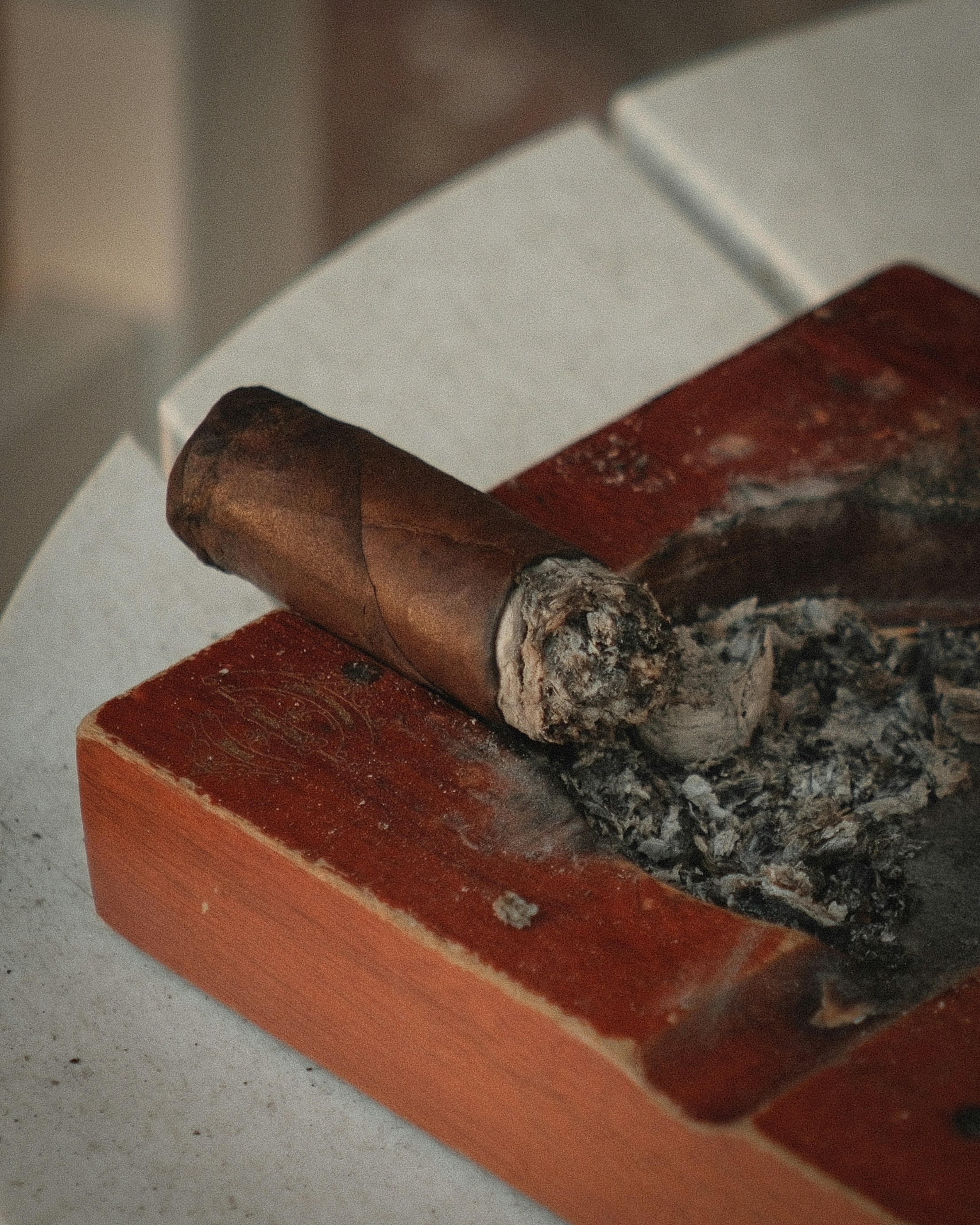 A lit cigar rests in a red wooden ashtray.