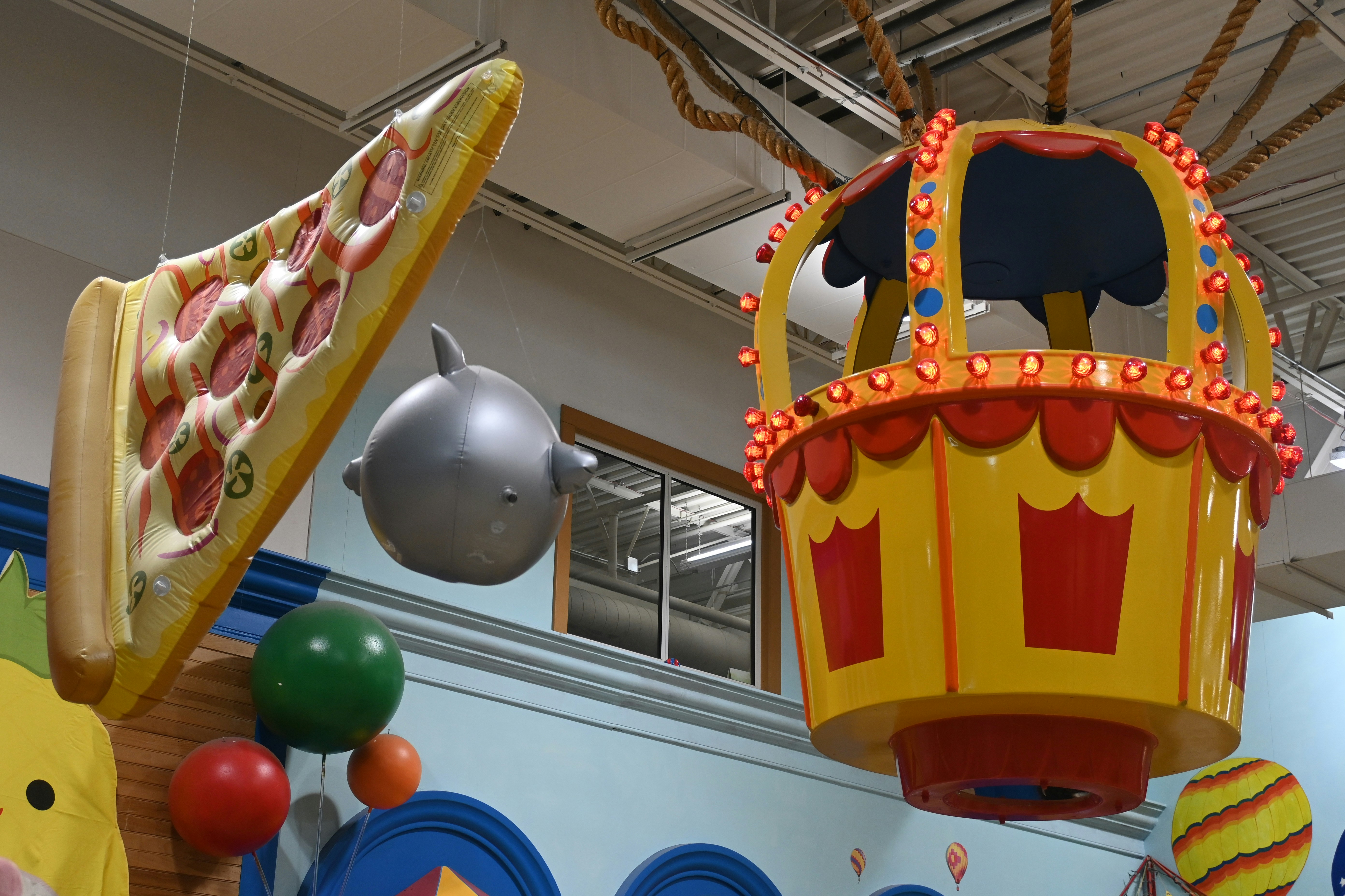 Floating Arcade: A Giant Pizza Slice and Balloon Basket Hover in a Playful Amusement Hall