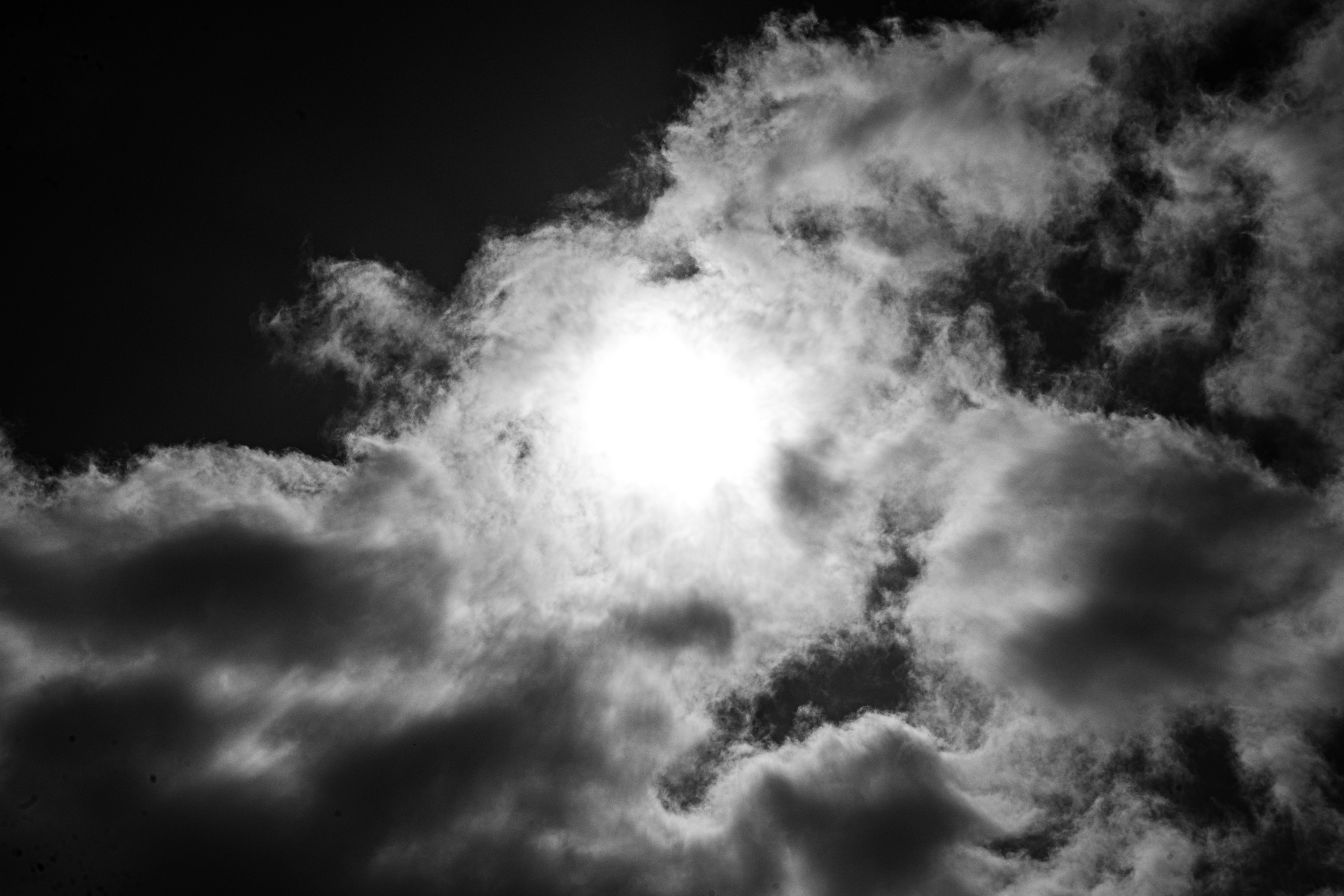 High-contrast monochrome sky with the sun piercing through thick clouds, emphasizing dramatic light and texture.