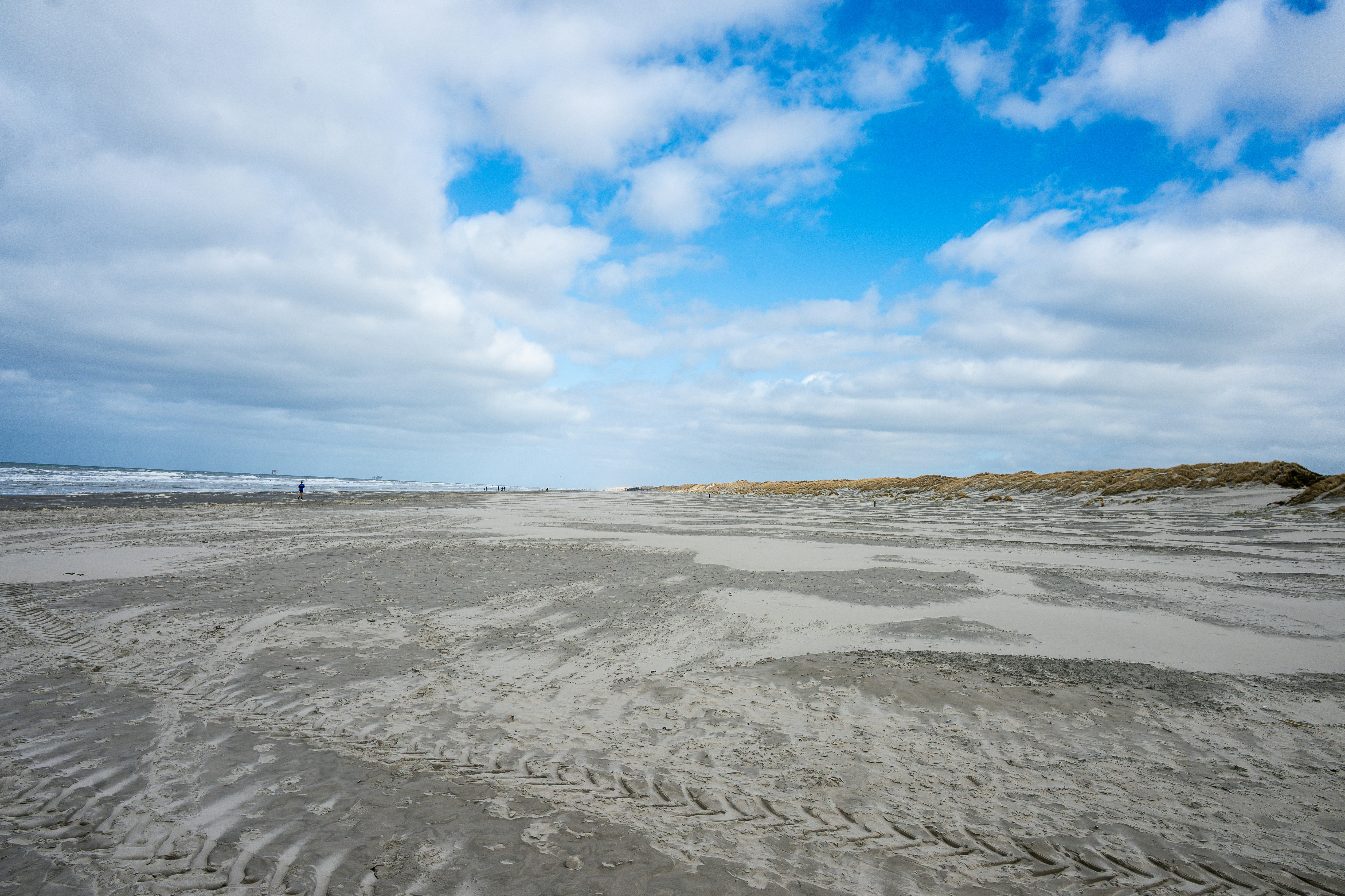 Wide sandy beach with ocean, dunes, and cloudy blue sky.