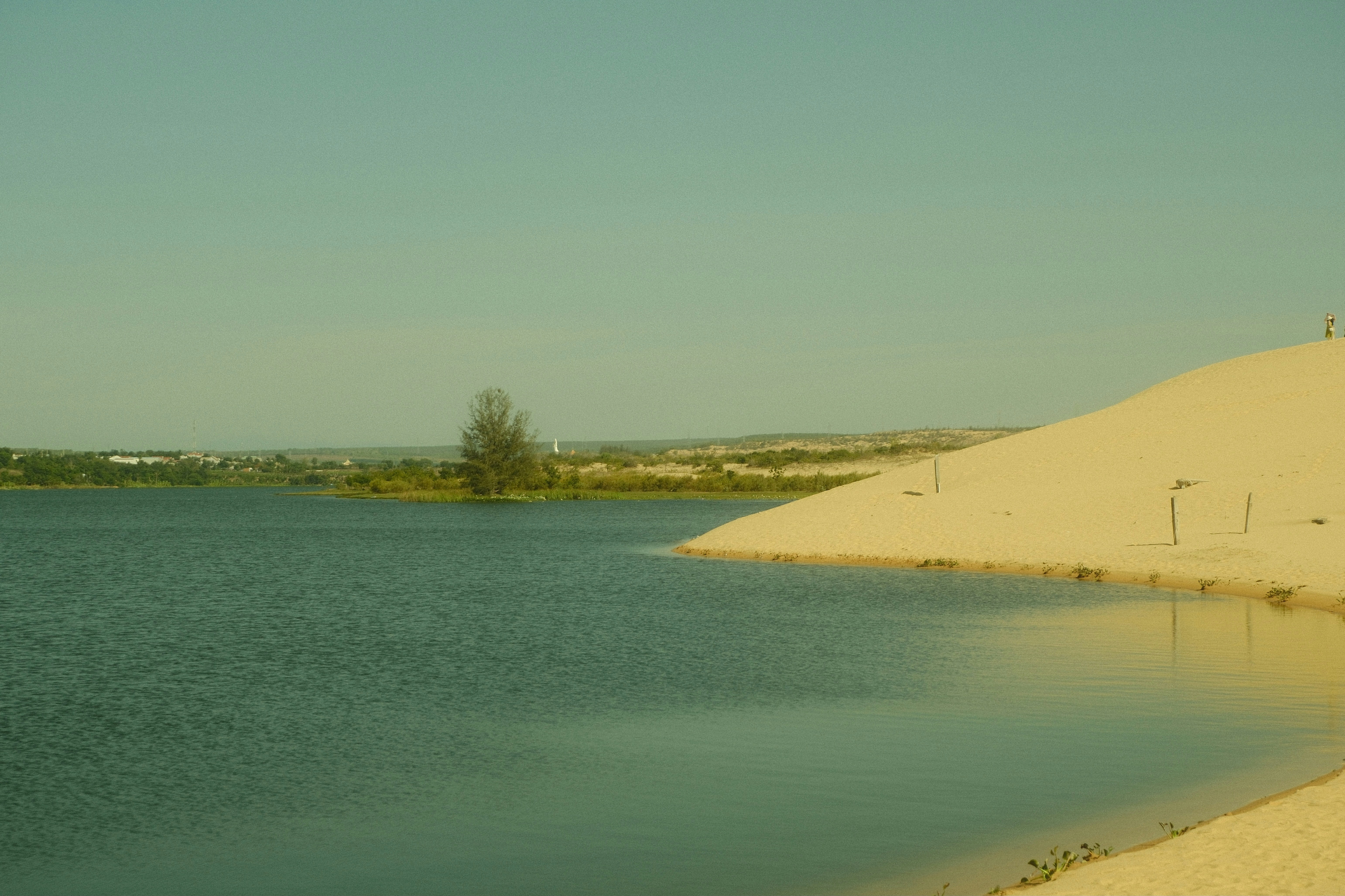 Sandy dune by a calm lakeshore under a turquoise sky