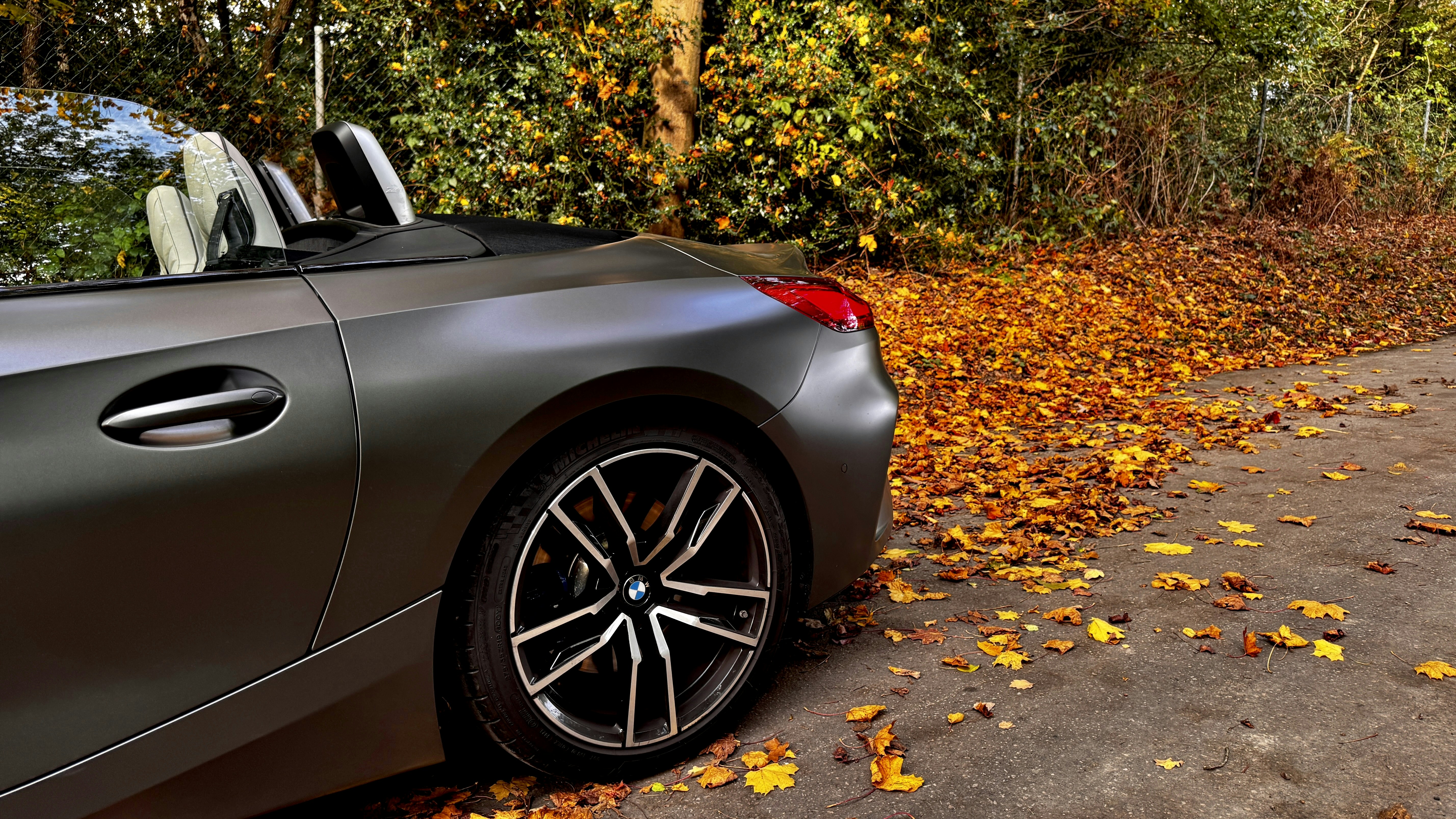 Matte Convertible in Autumn Light, Wheel-Rim Shadows on a Leaf-Covered Drive