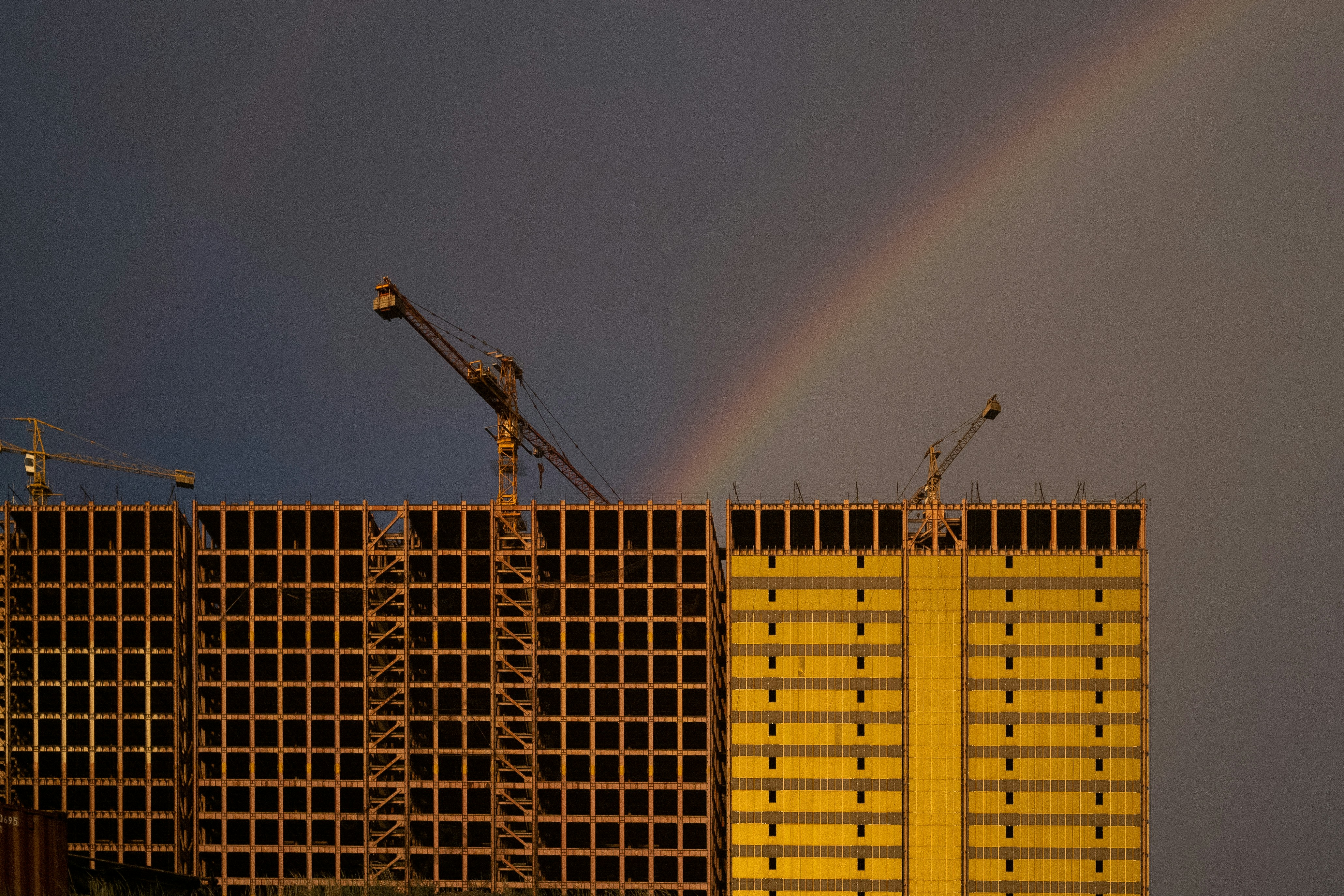Rainbow over a building under construction with cranes.