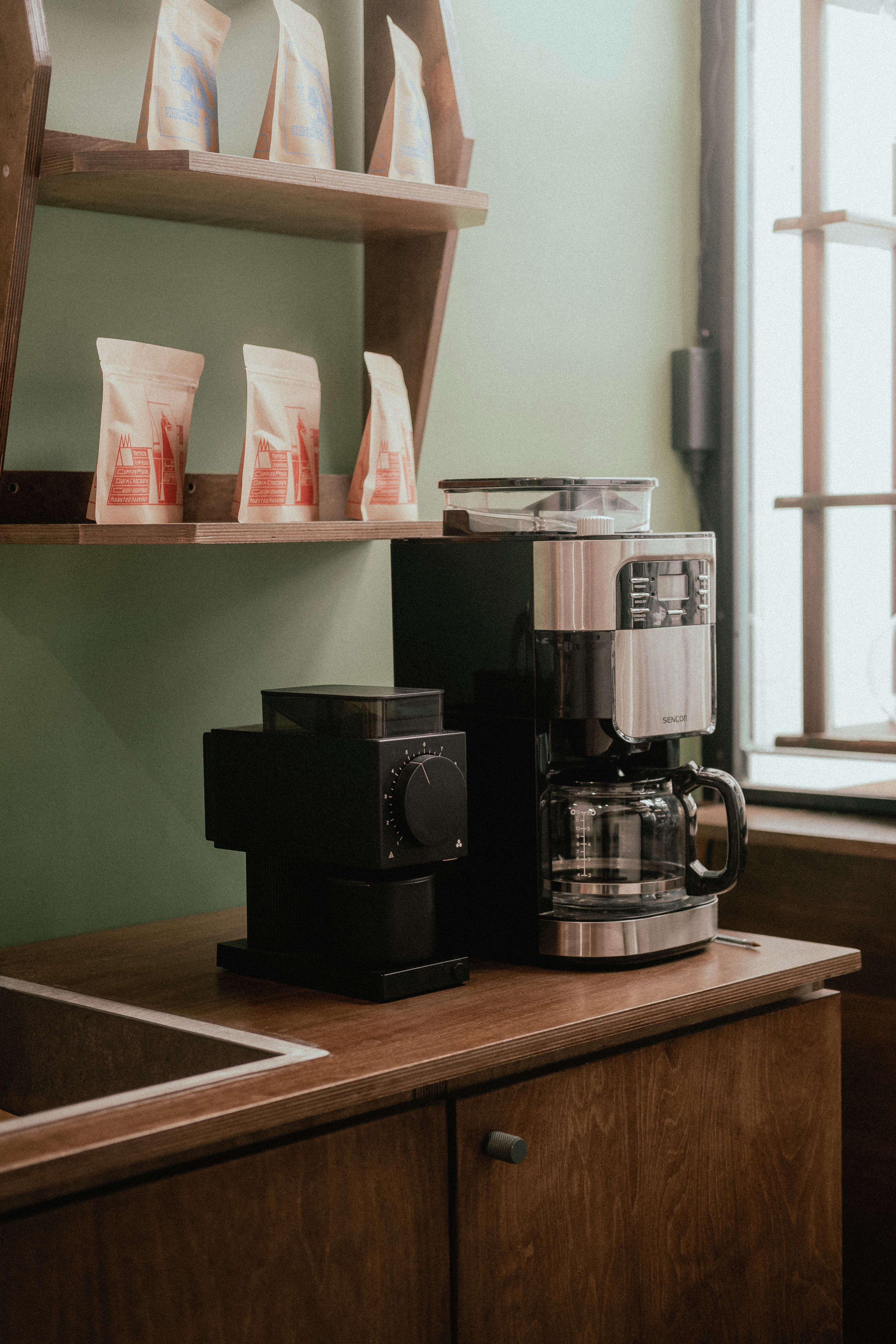 Coffee grinder, maker, and bags on a wooden counter.