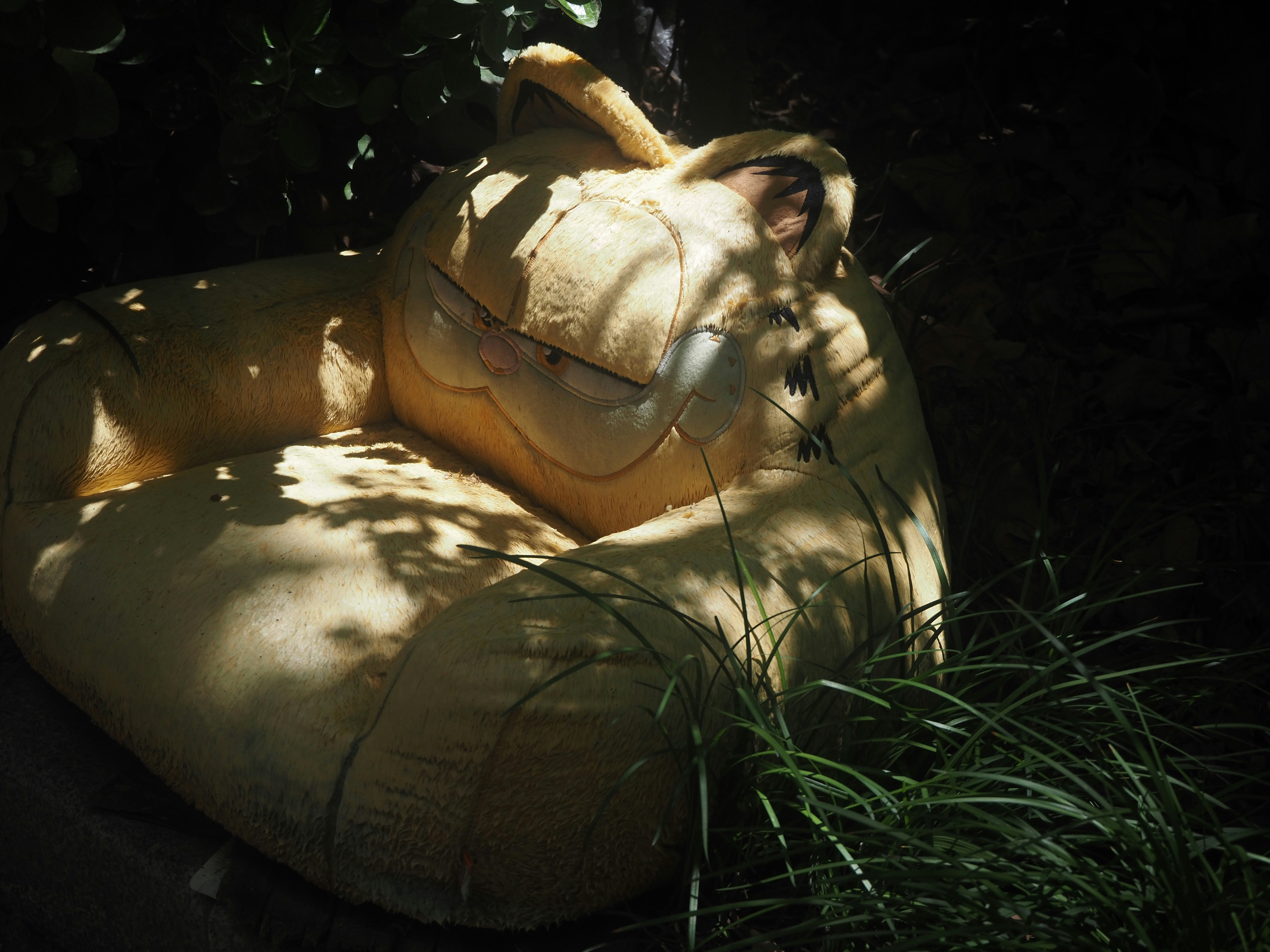 Deflated yellow inflatable character resting in shadows and green grass.