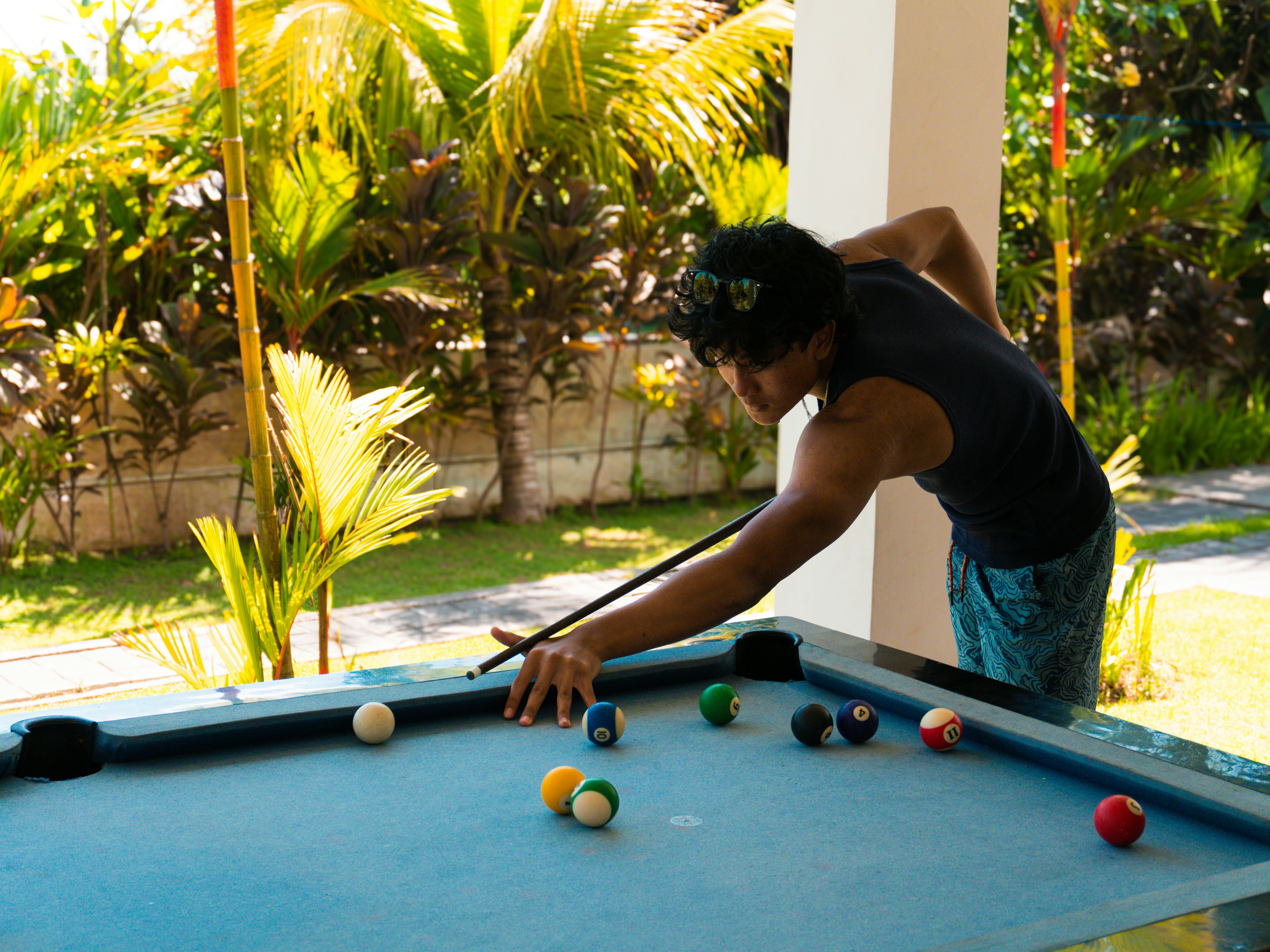 Man playing pool on a blue table surrounded by greenery.