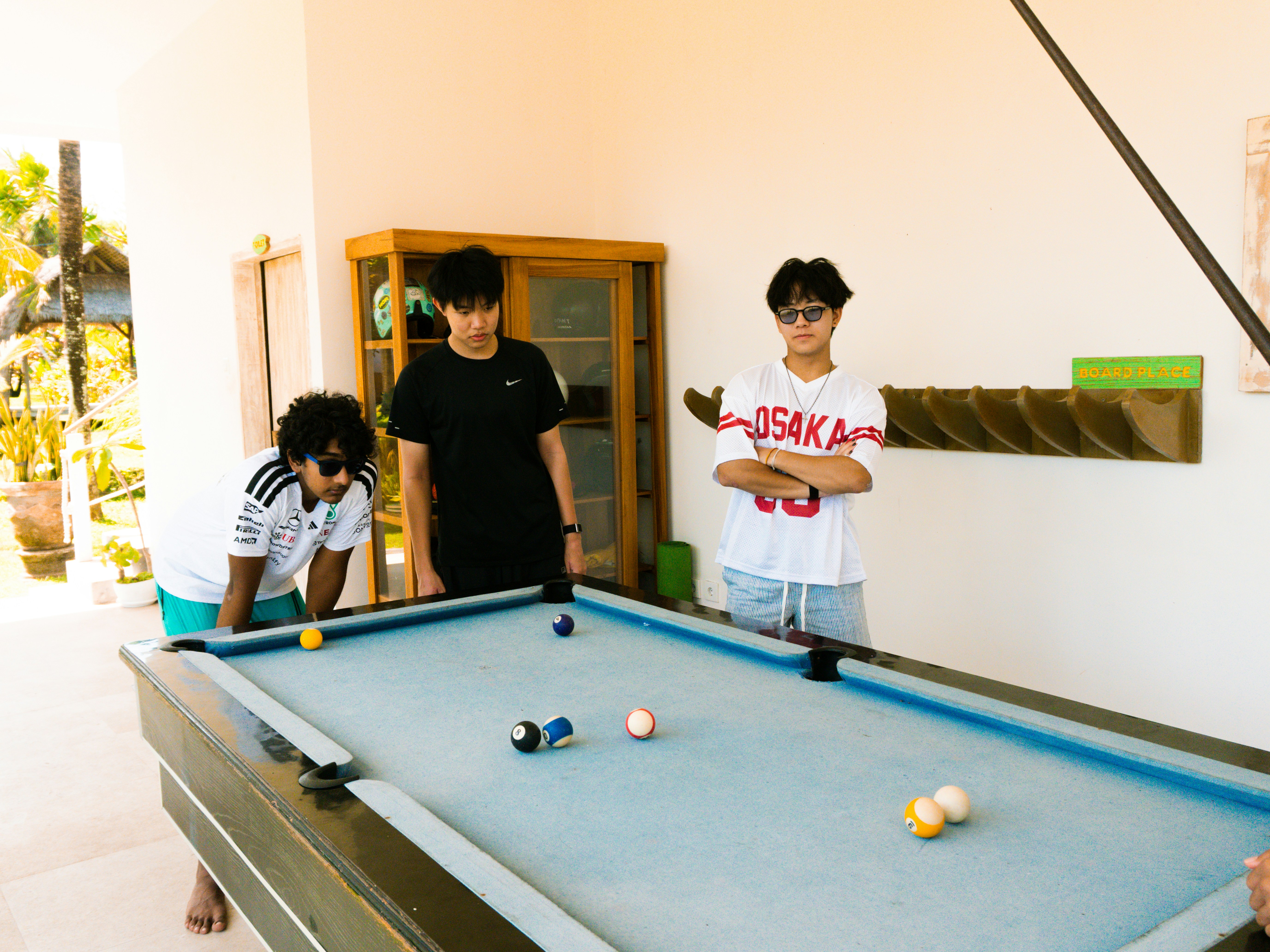 Three young men playing pool on a sunny day.