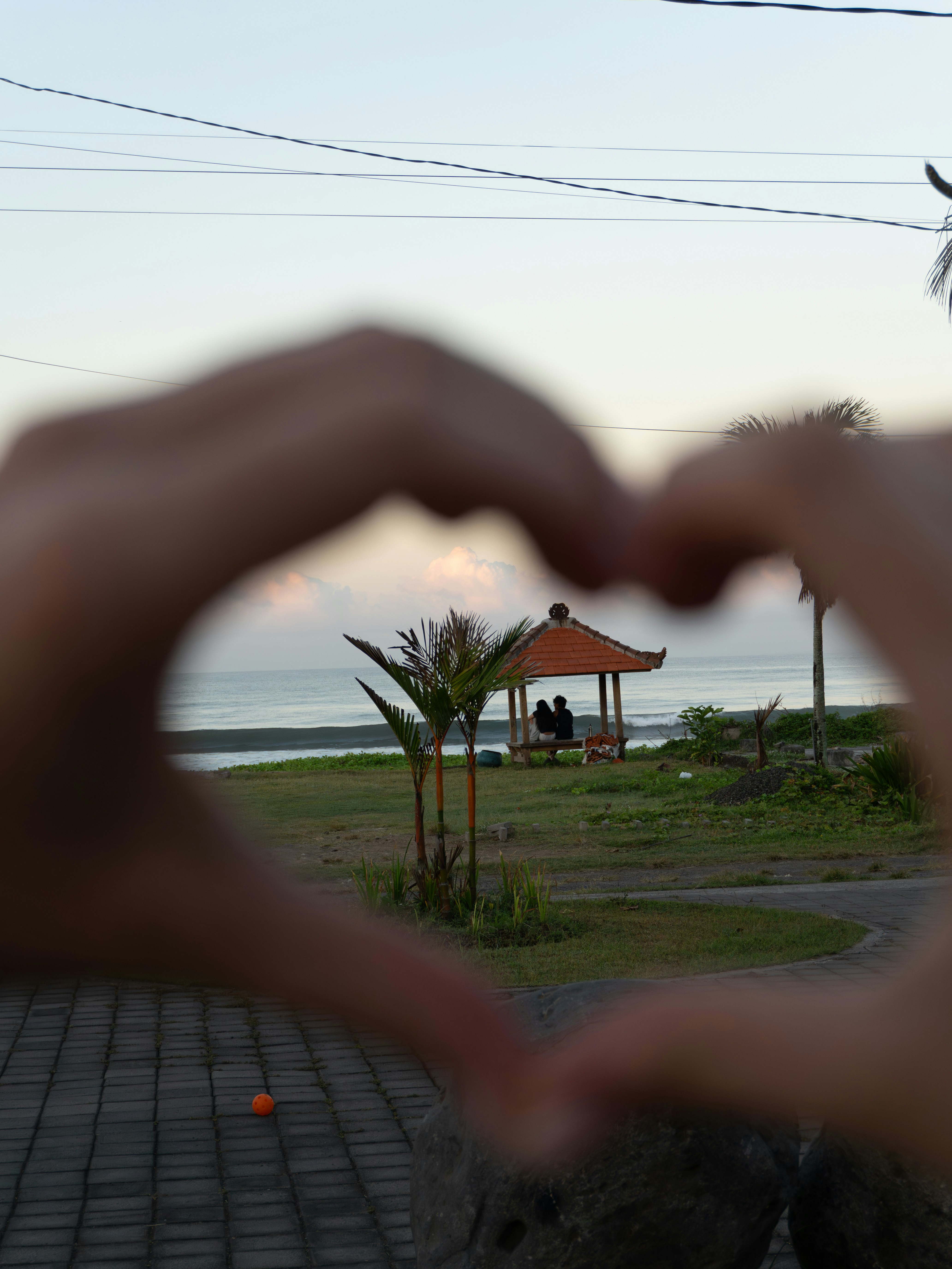 Hands form heart shape framing couple in gazebo by ocean.