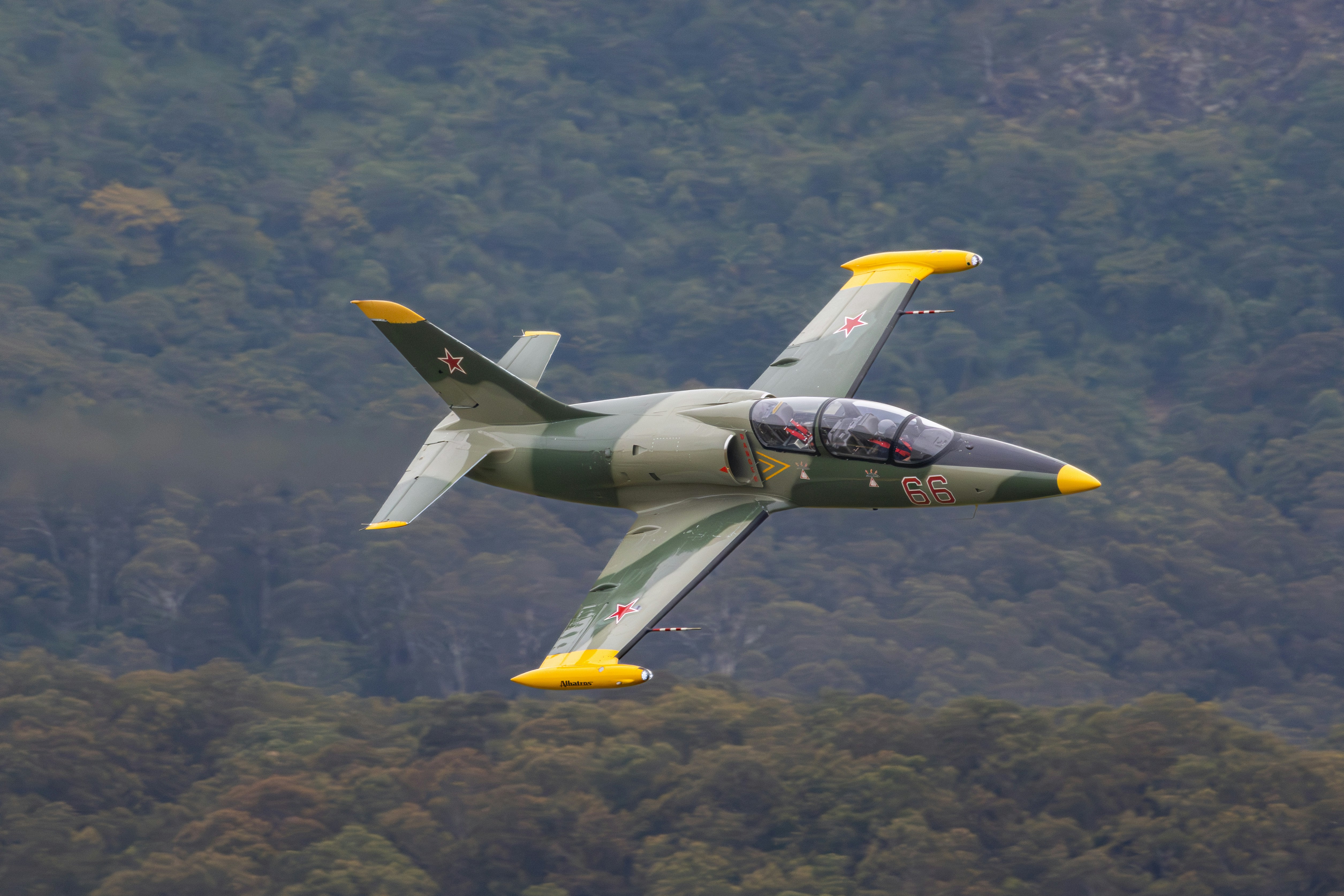 Yellow-tipped Soviet-era jet in mid-flight over forested backdrop