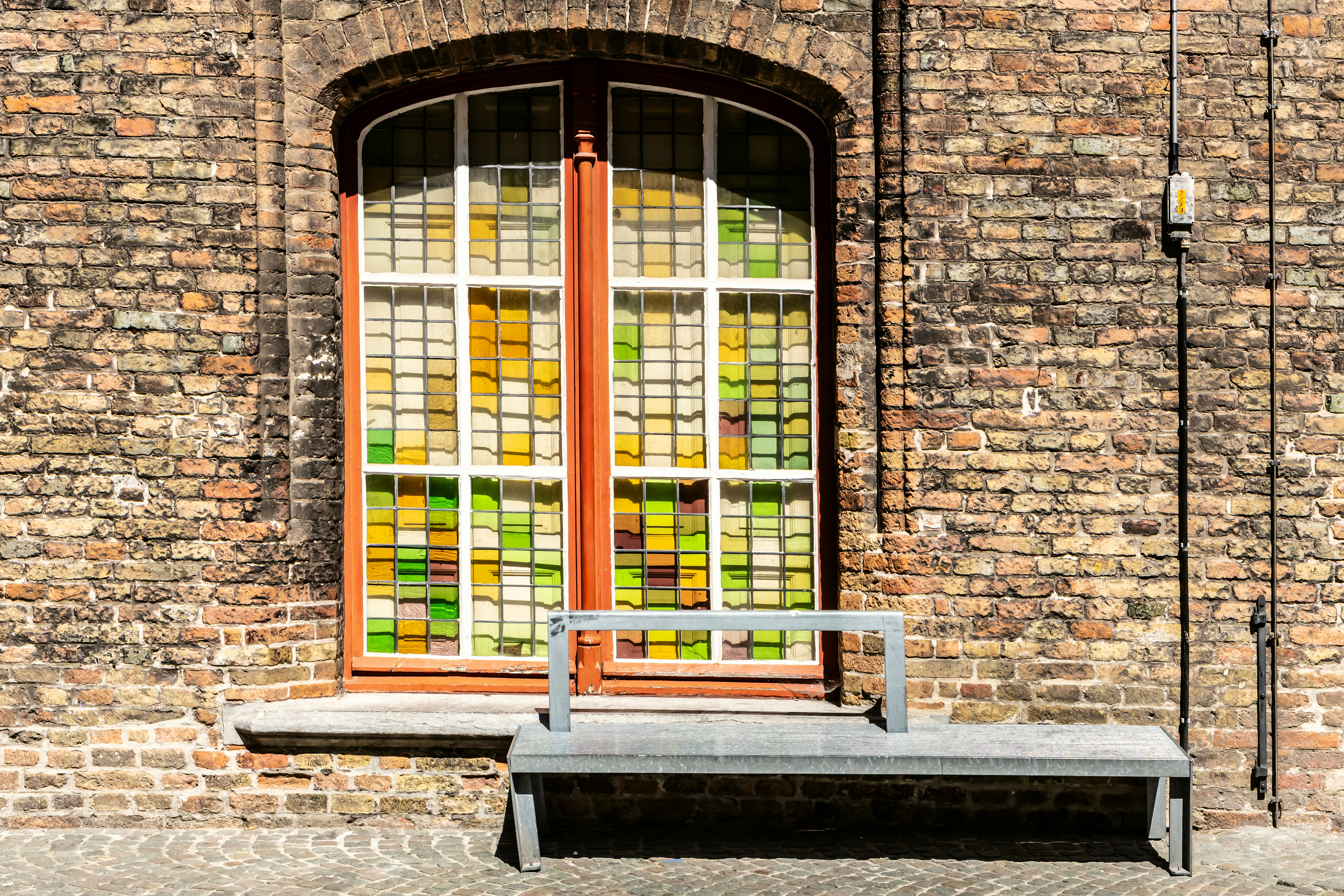 Stained Glass Window Framed by Brickwork on a Quiet Cobblestone Wall