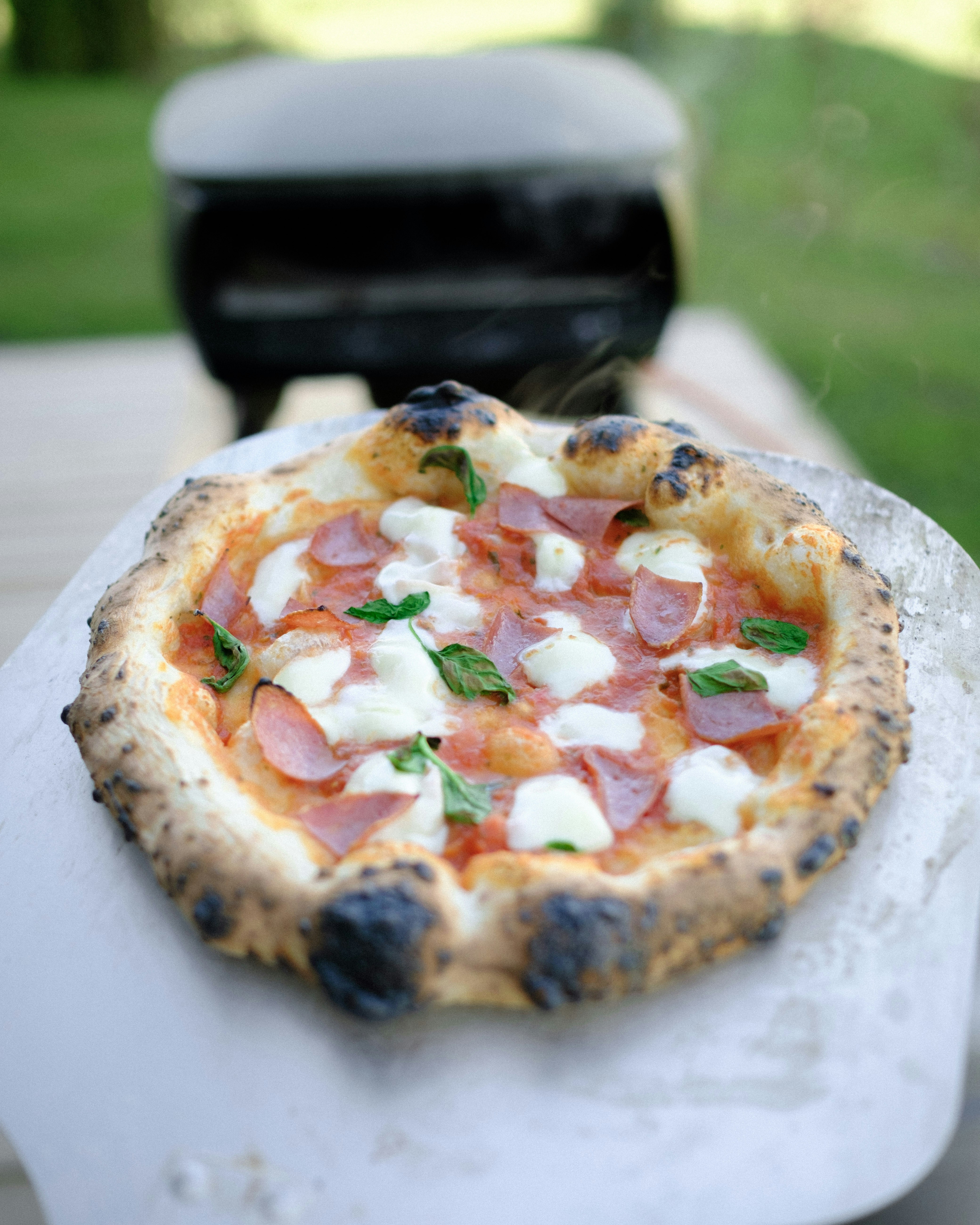 Neapolitan pizza with ham, mozzarella, and basil from outdoor oven.