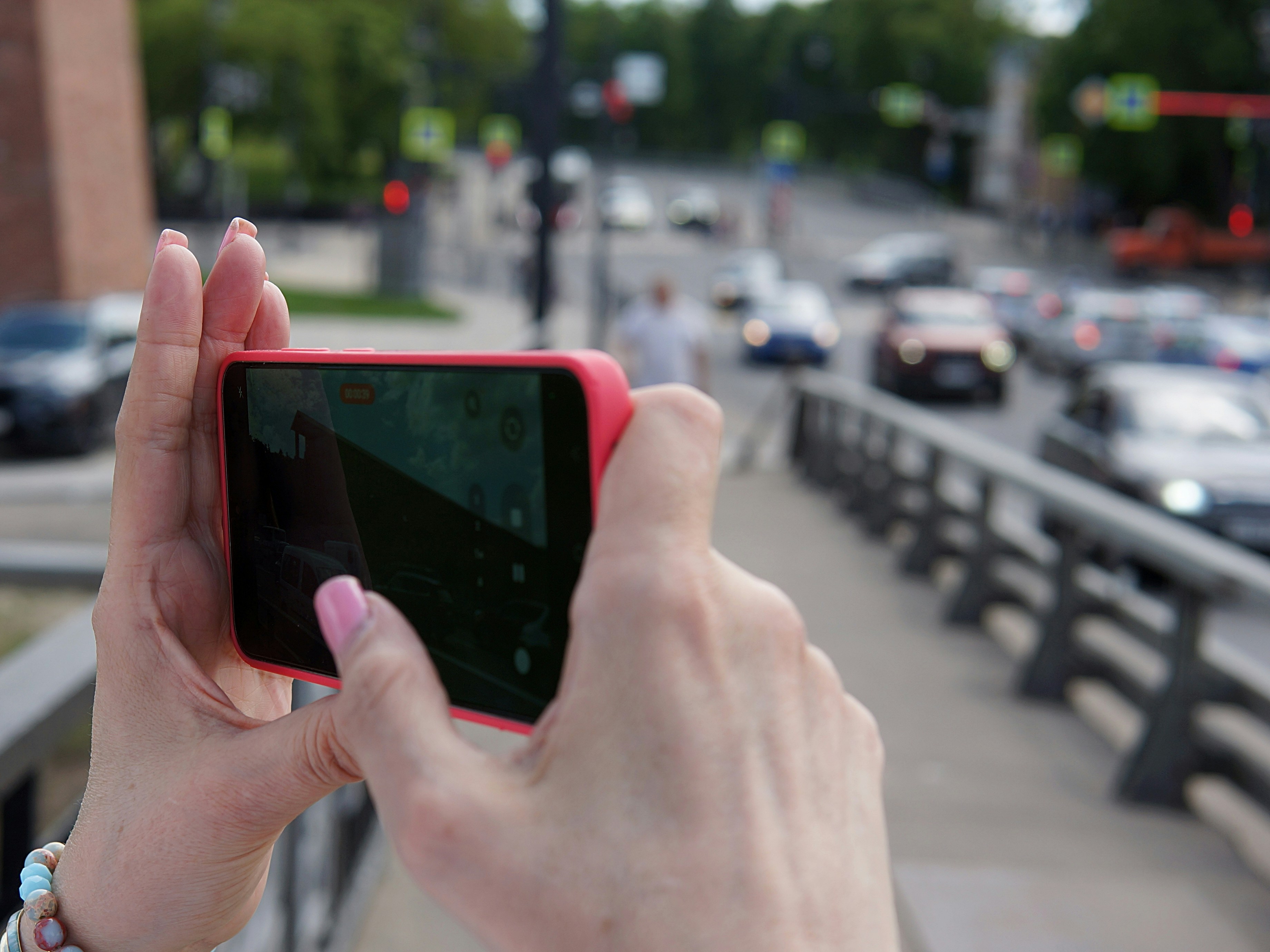 Hands holding a red smartphone, recording a blurred city street.