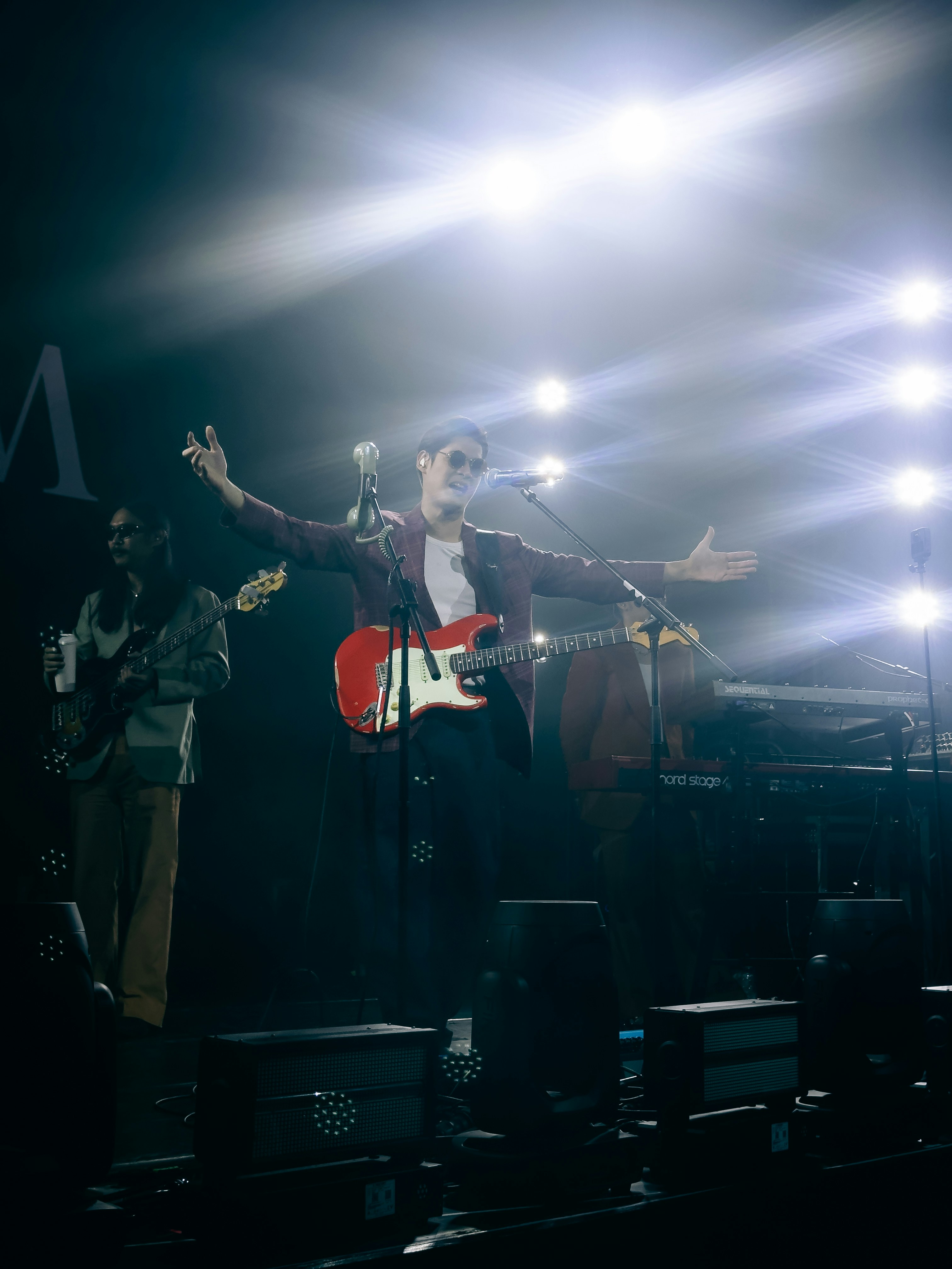 Musician with red guitar on stage under bright lights.