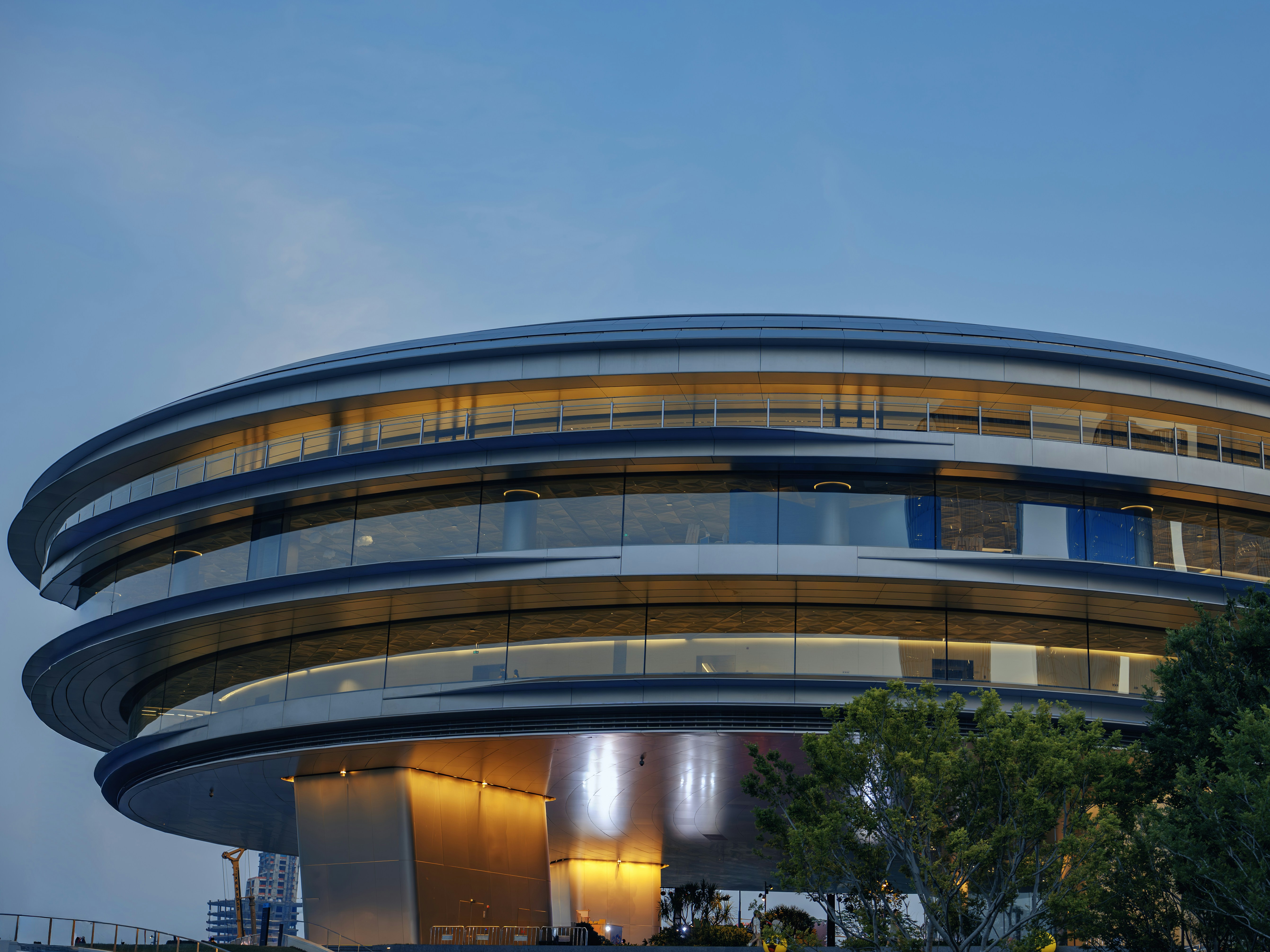 Orbiting Glass: The Circular Office Tower Ascends Over a Green Foreground