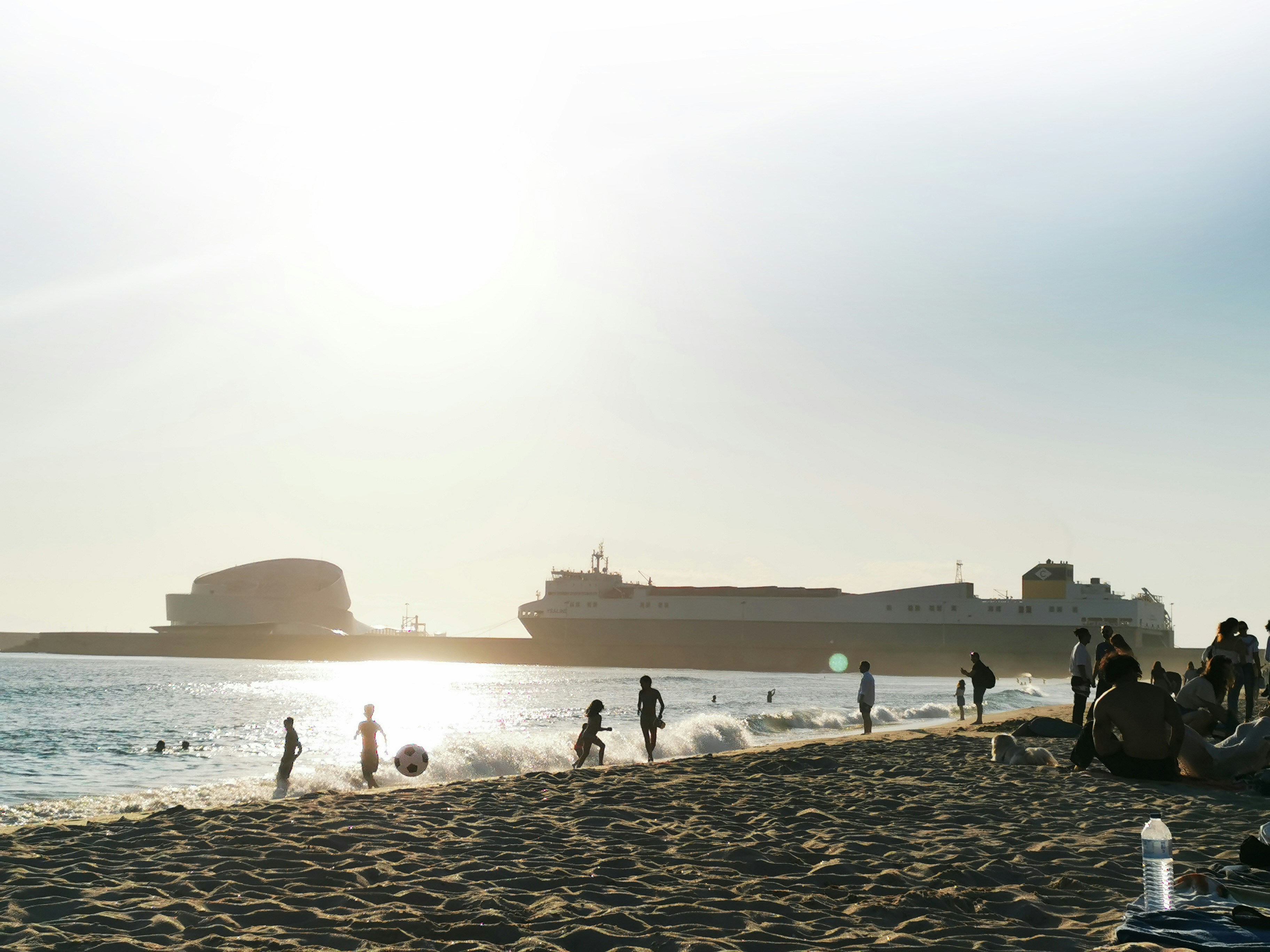 Sunlit shoreline vs. distant harbor: a tranquil beach scene with ships on the horizon