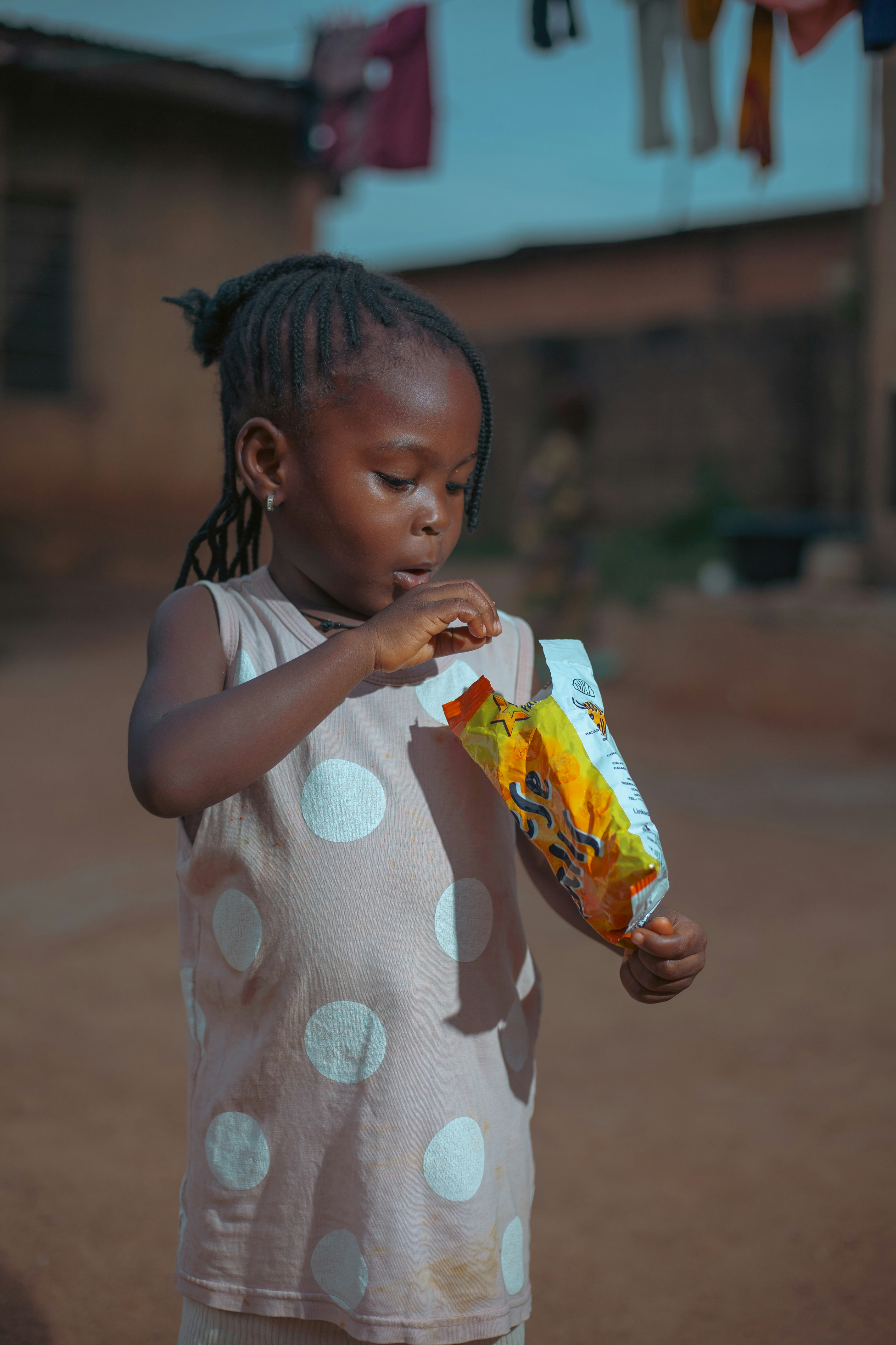 A young girl eating snacks from a bag outdoors.