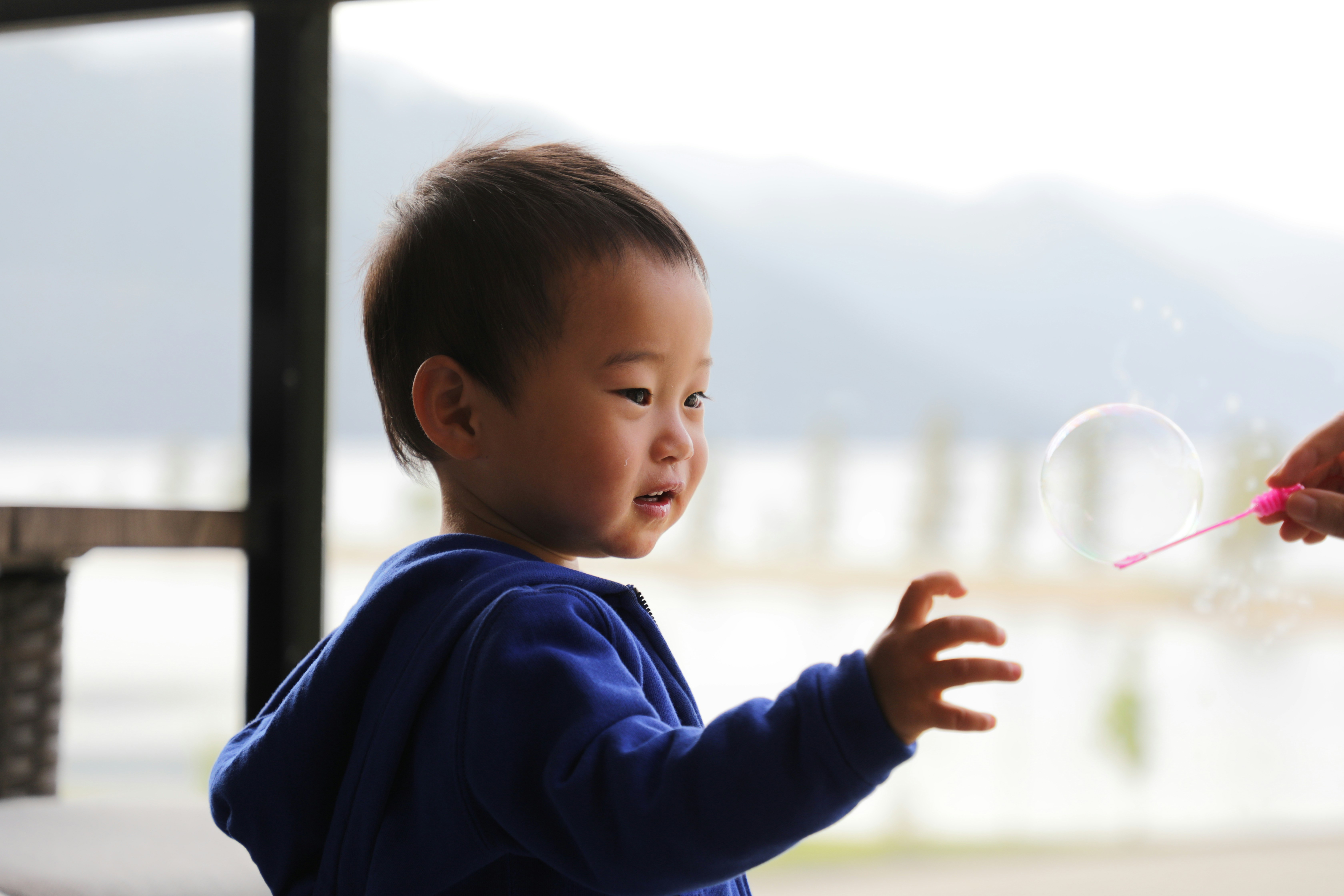 Bubble Play: A toddler reaches toward a delicate dream at the glass window