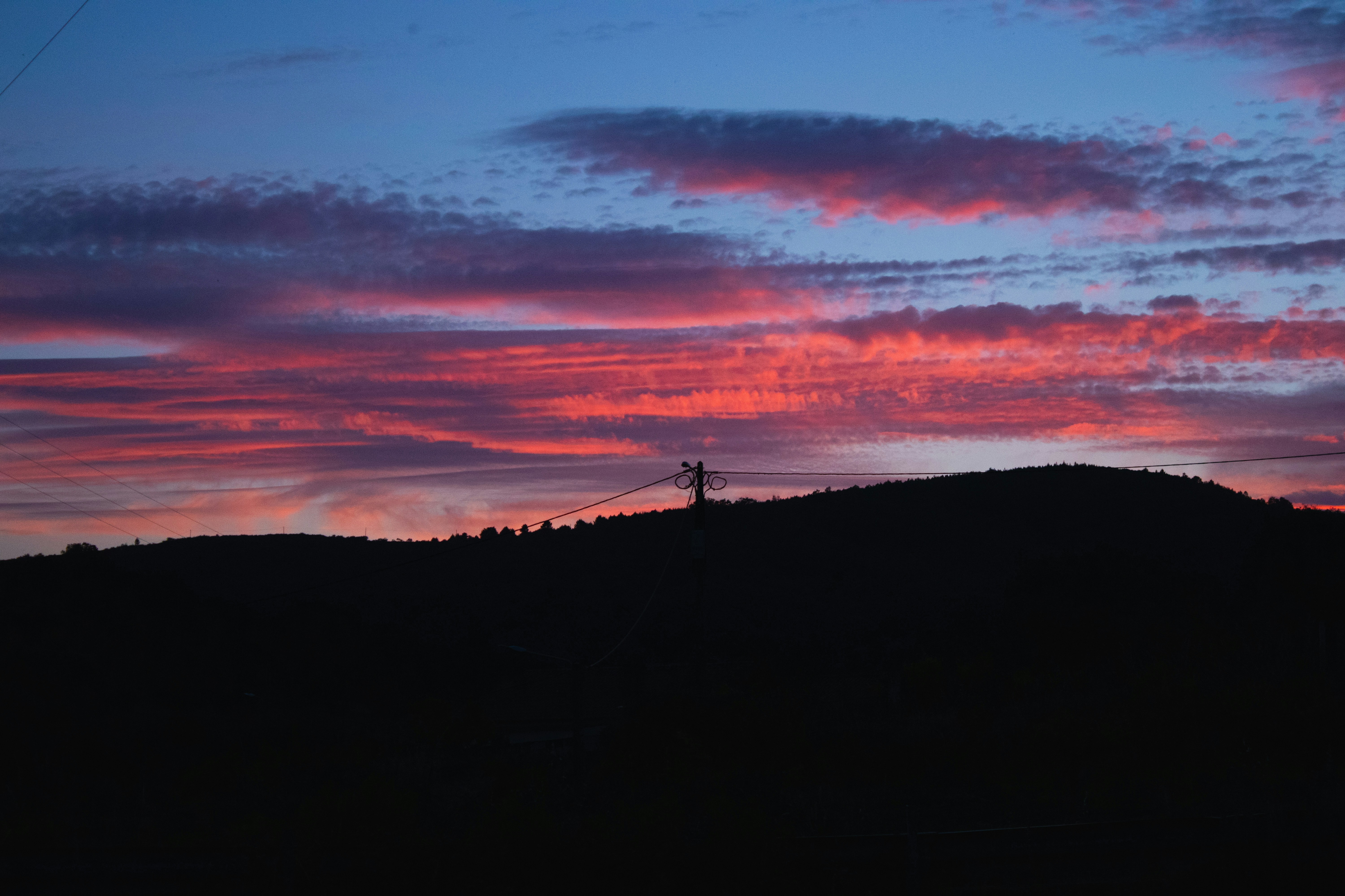 Silhouetted ridge at dusk with a lone mast under pink-tinged clouds