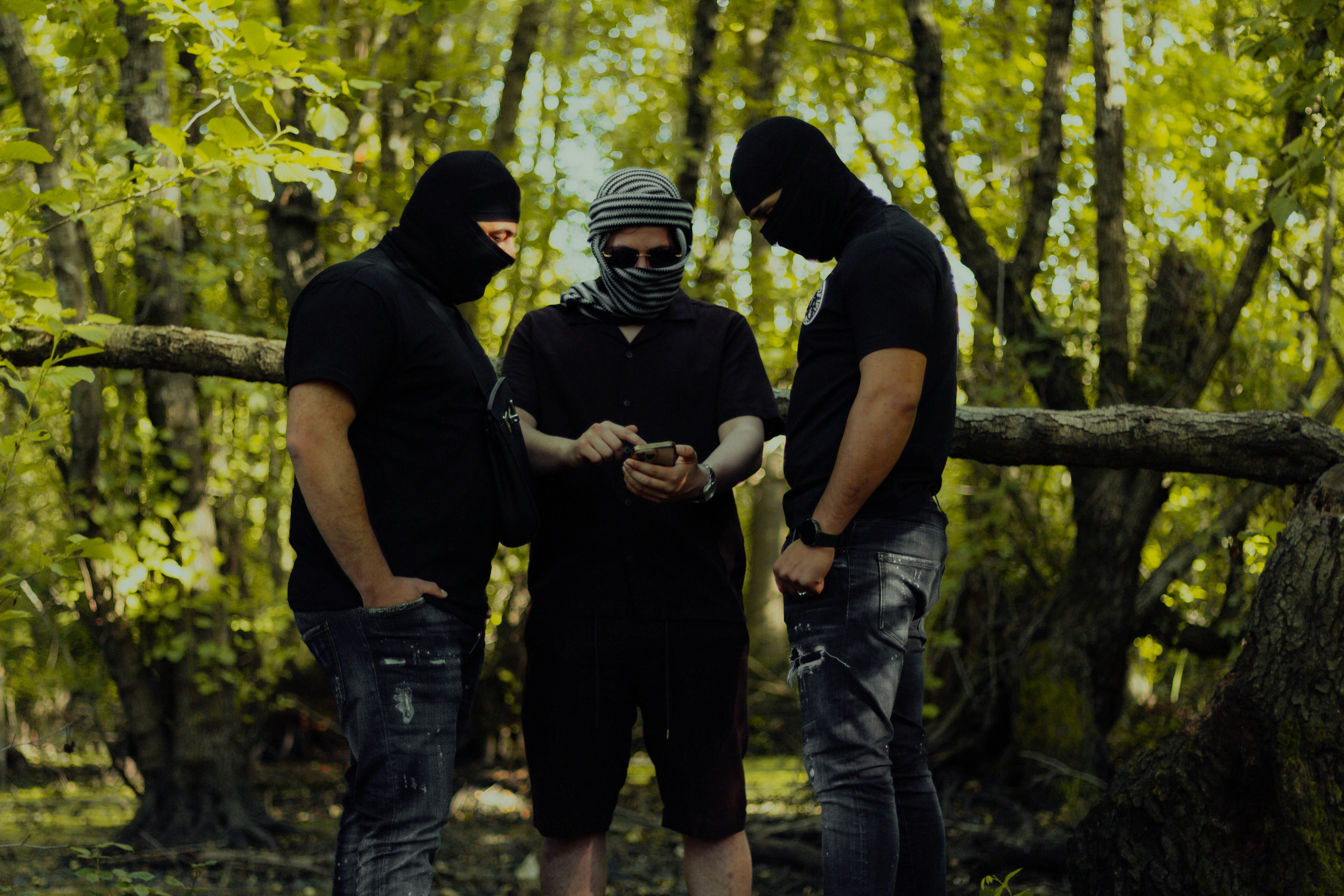 Masked trio in a sun-dappled woodland discussion over a handheld device