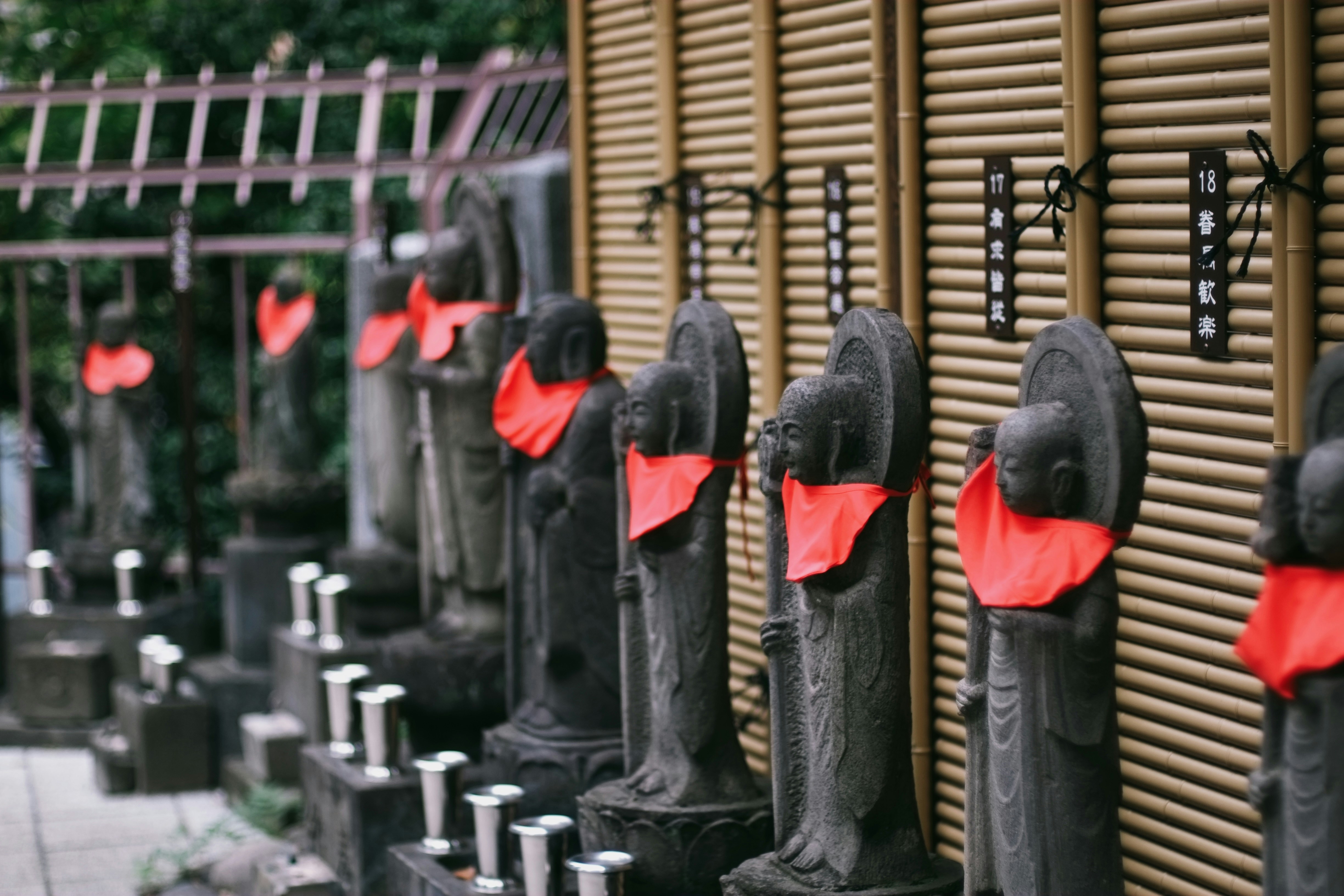 Row of stone Buddhist statues with red bibs at a Shinto temple facade