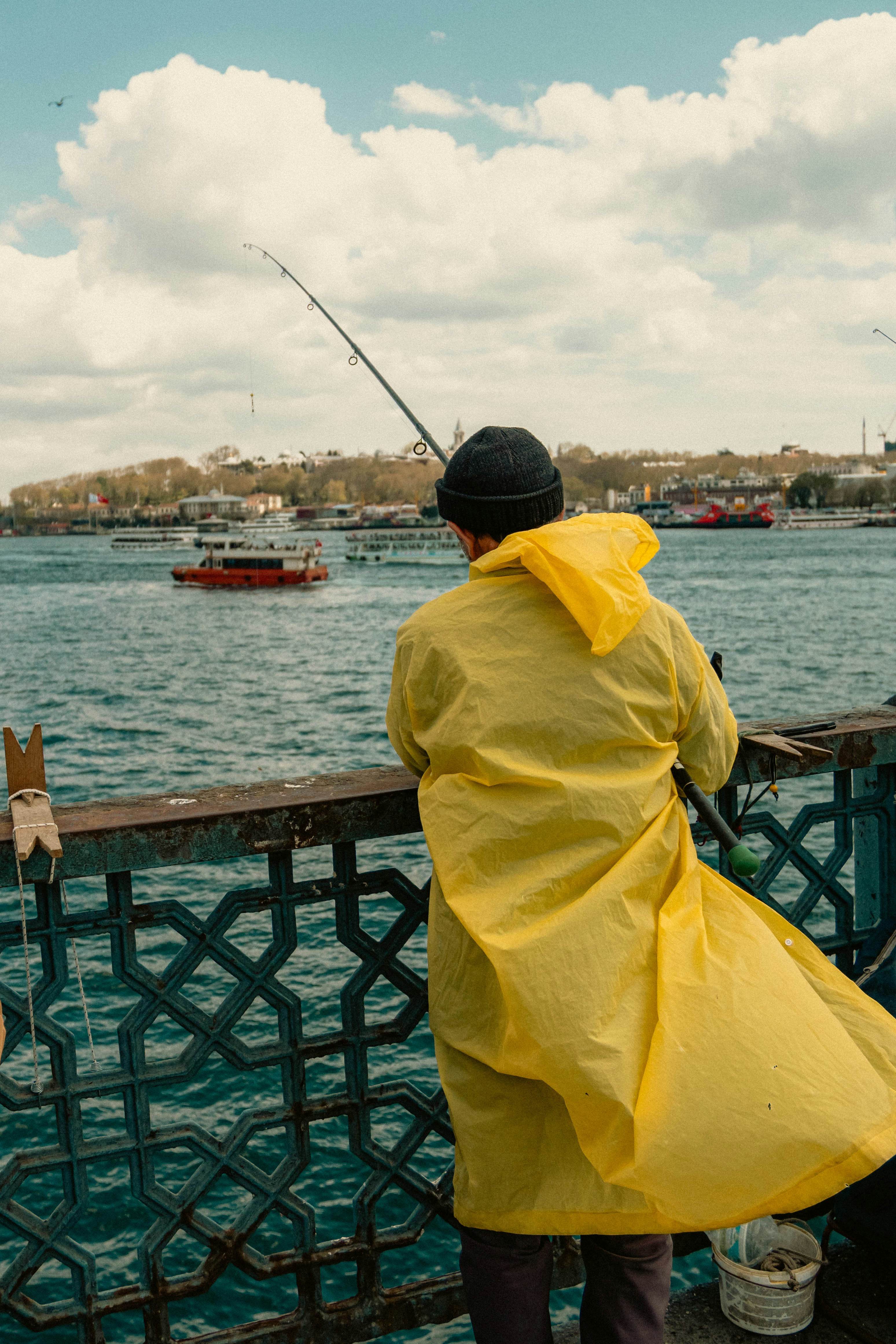Person in yellow raincoat fishing from a bridge.