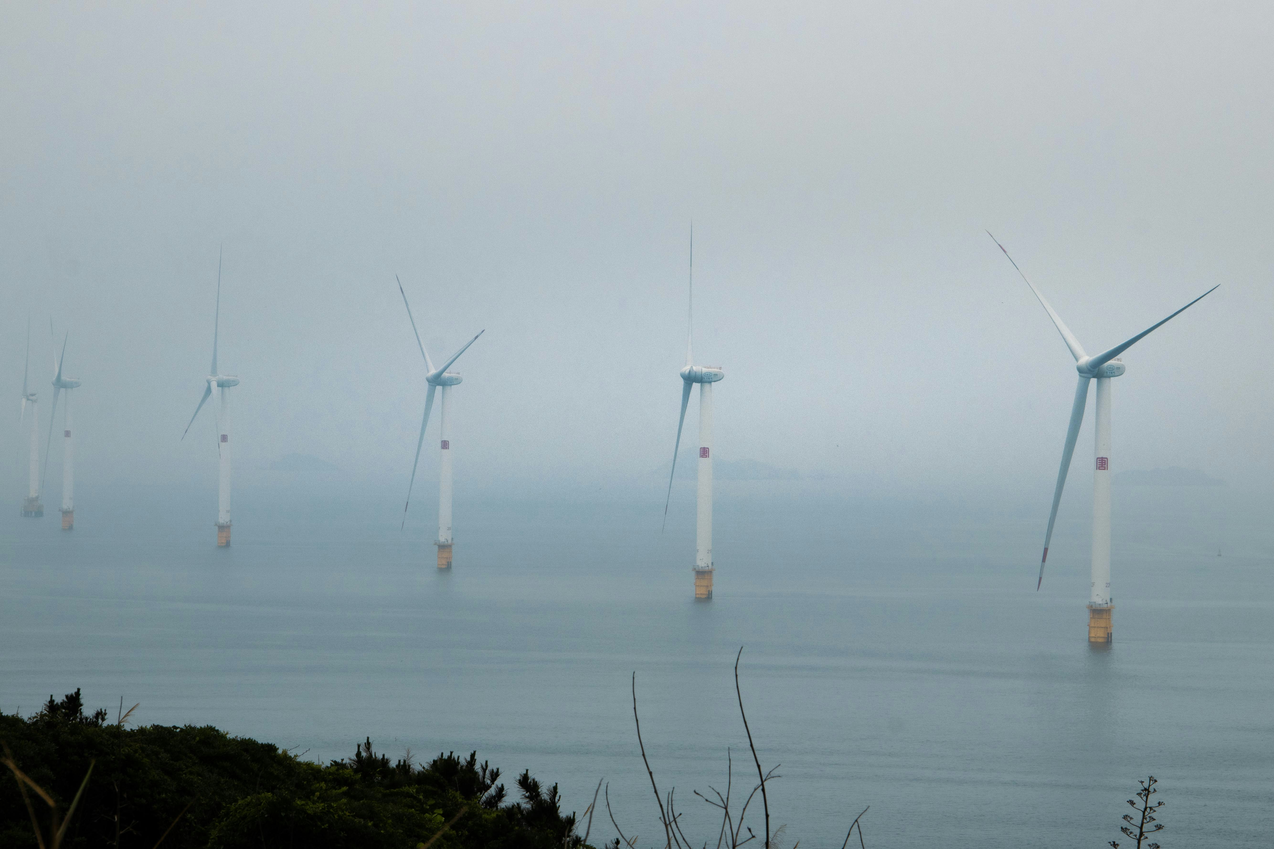 Whispering Giants: Offshore Wind Turbines Piercing a Hazy Sea