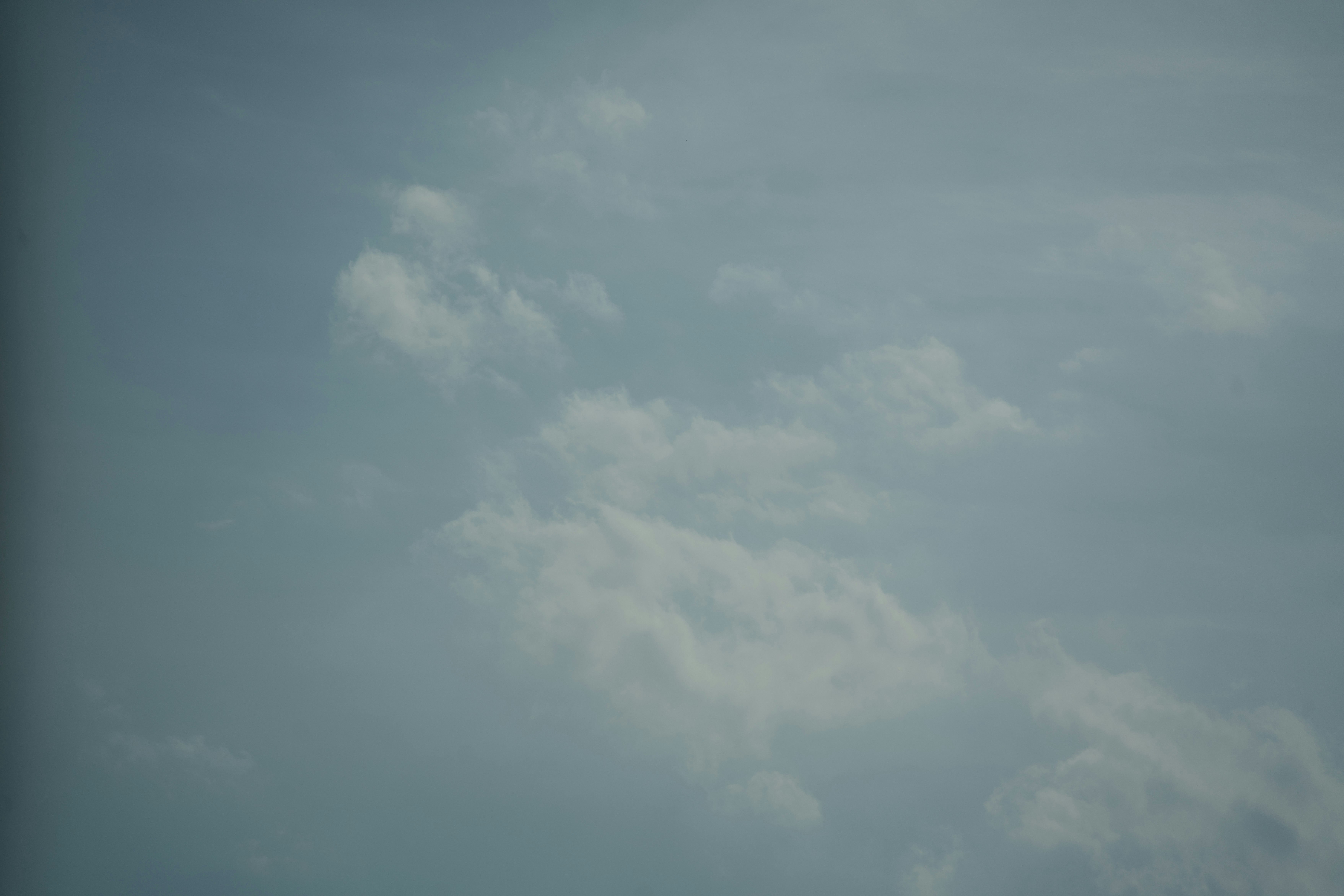 Soft blue sky with light, scattered clouds framed by a subtle dark vignette along the left edge.