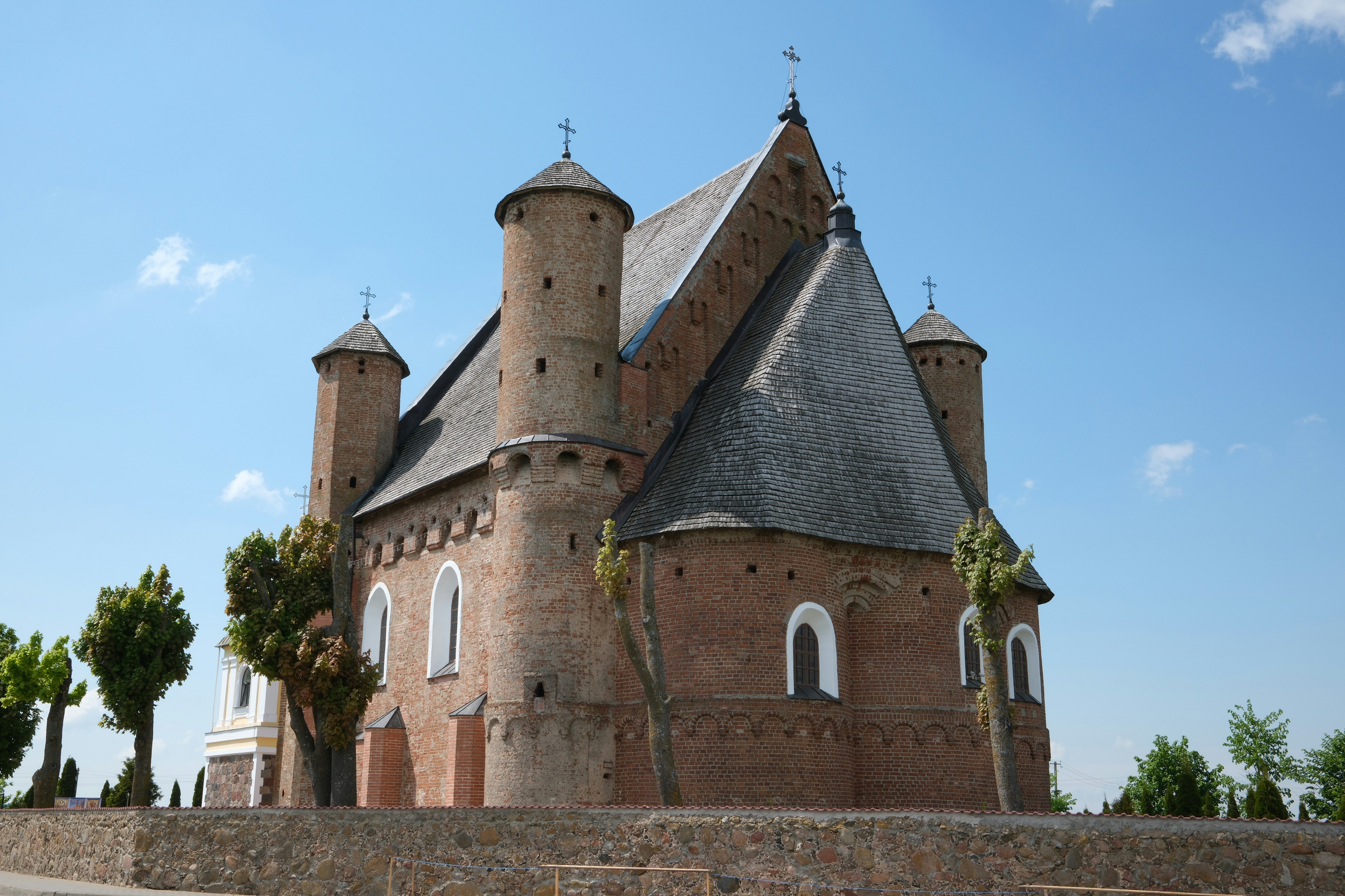 Medieval brick church rising from a low stone wall under a clear sky
