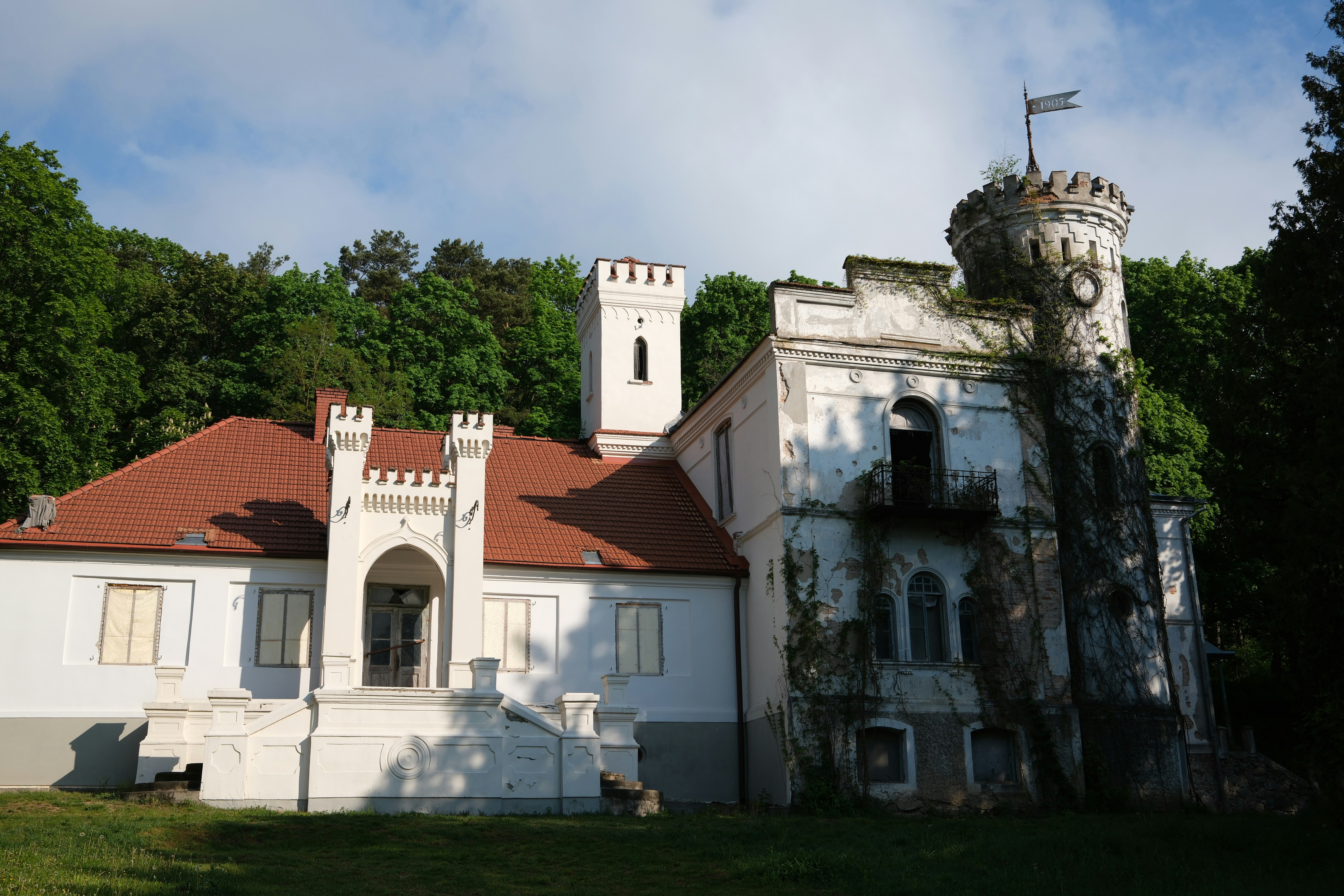 White manor house with a prominent tower and green forest.