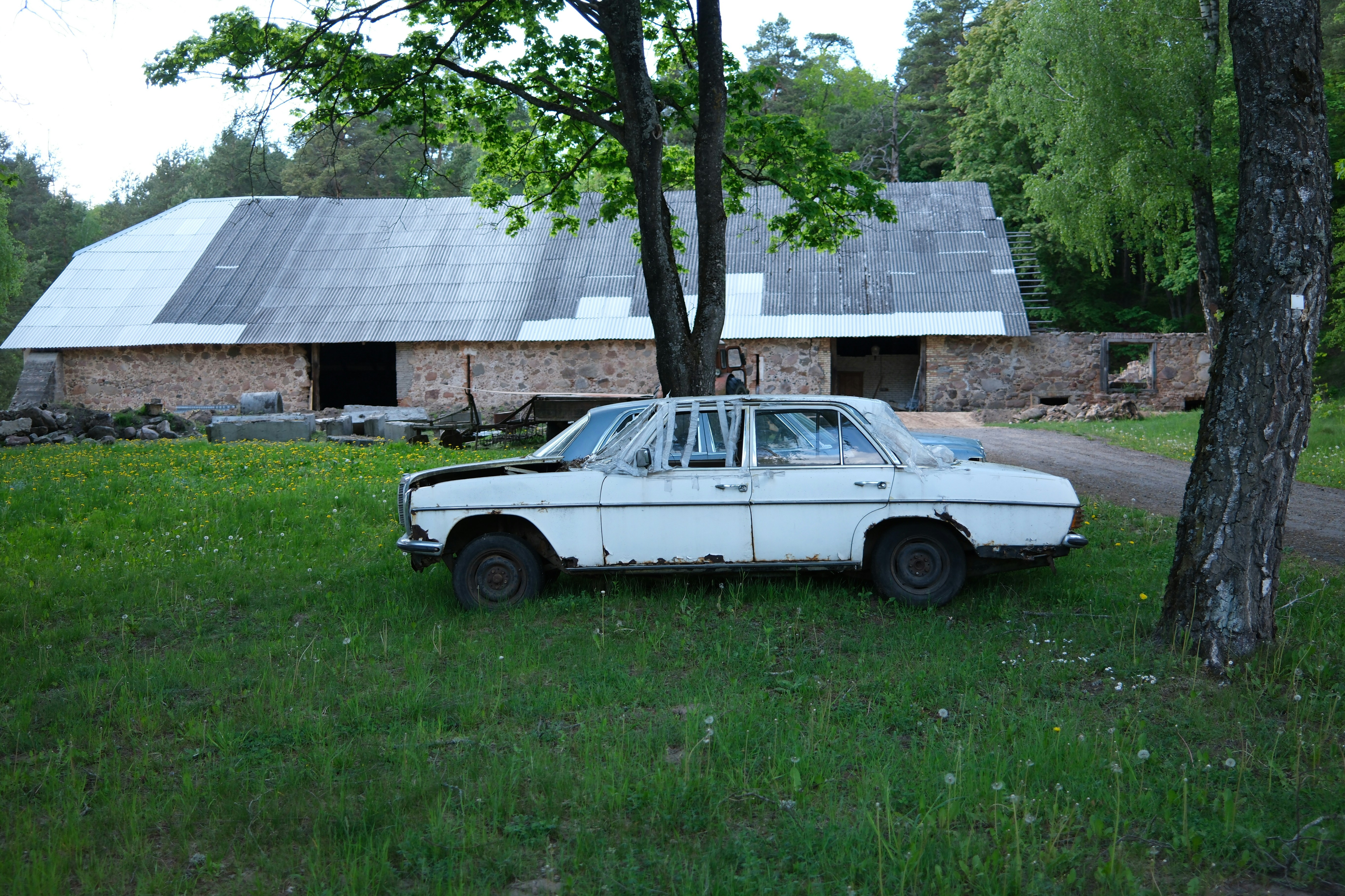 Old rusty white car parked in front of rustic building.