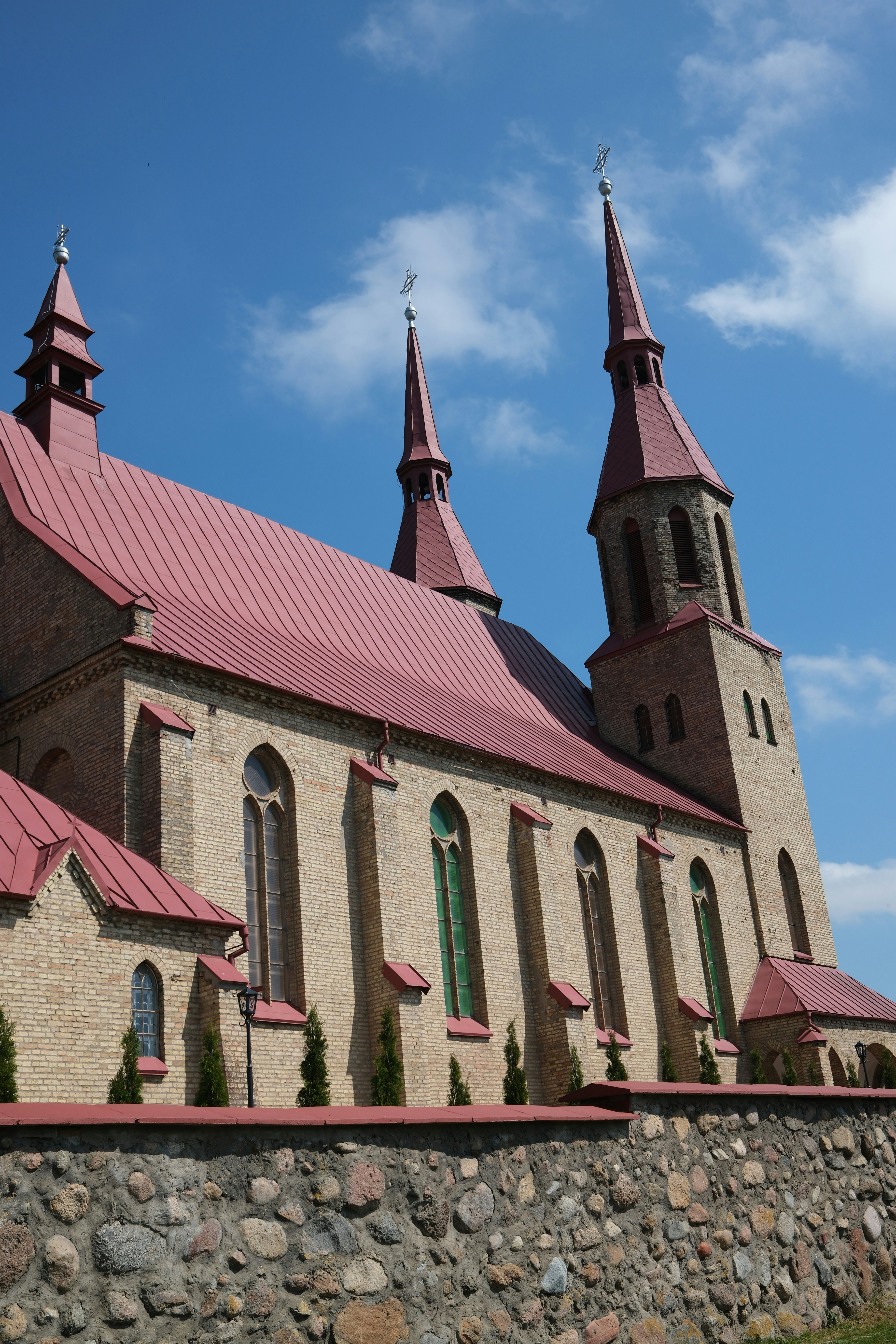 Red-roofed church rising above a stone boundary under a clear blue sky