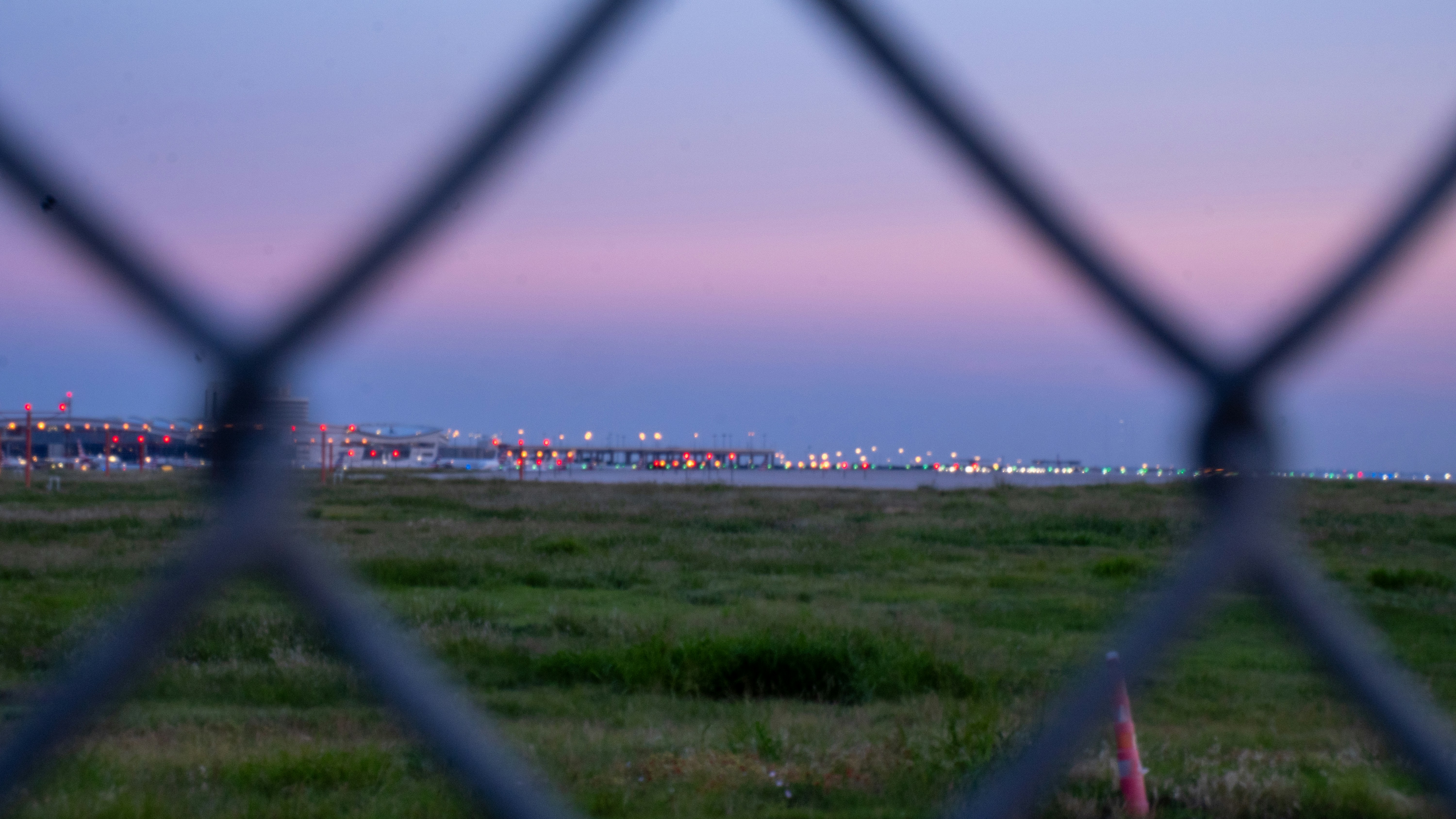 Through the Grid: Distant Runway Lights Beyond a Fence