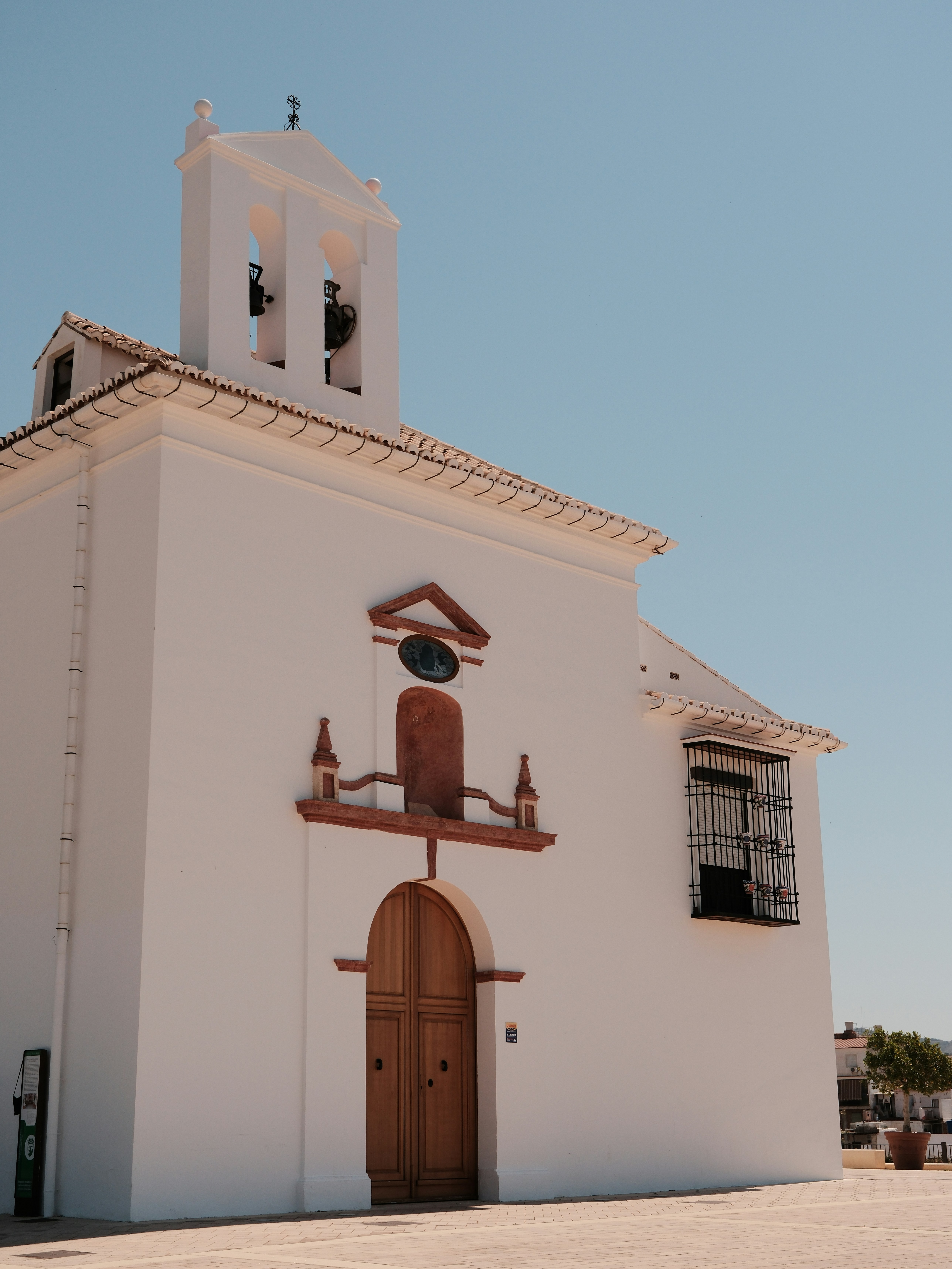 White Chapel with Wooden Doors Beneath a Small Bell Tower under Clear Blue Sky