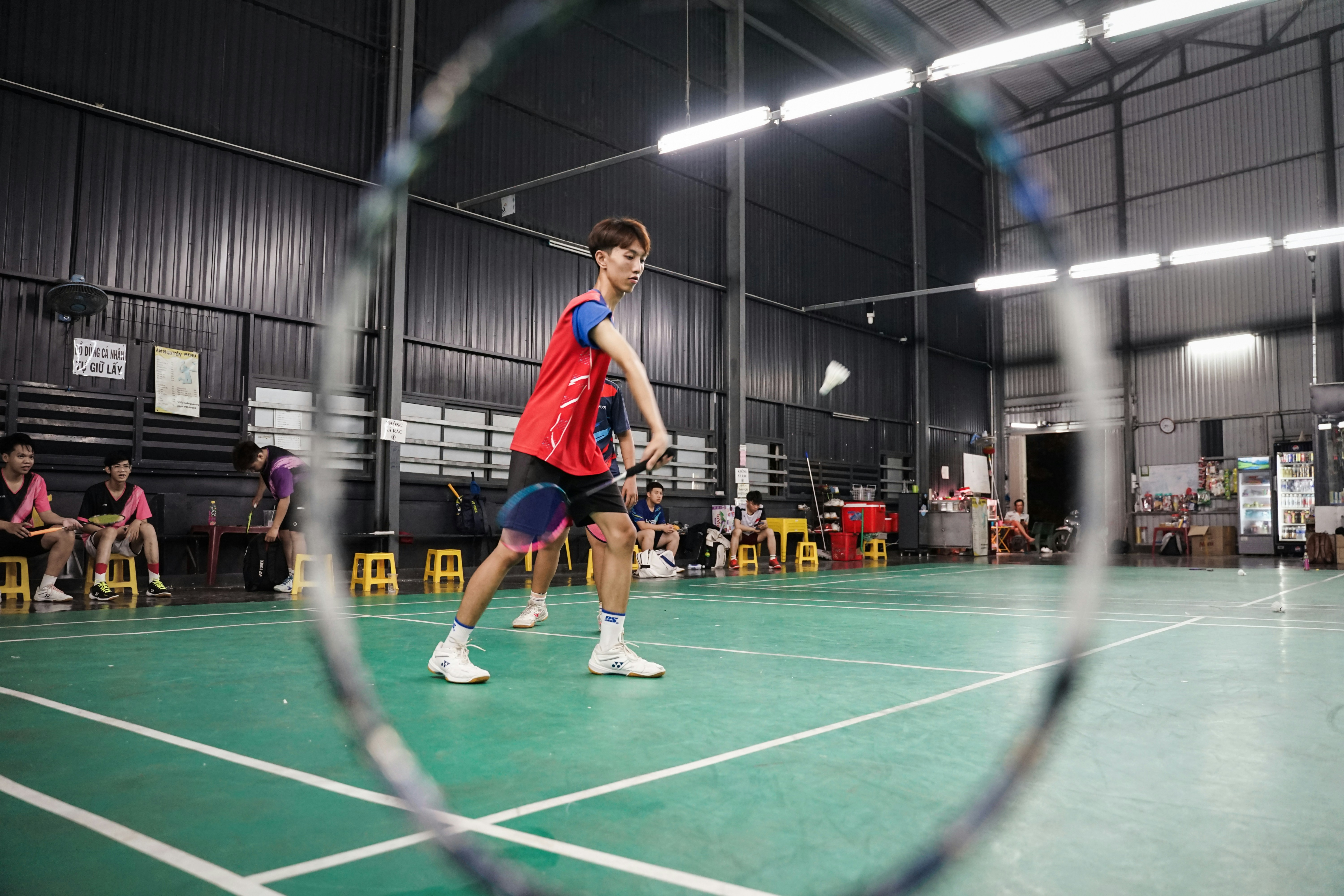 Mid‑match Focus: A badminton player in action within a gym arena