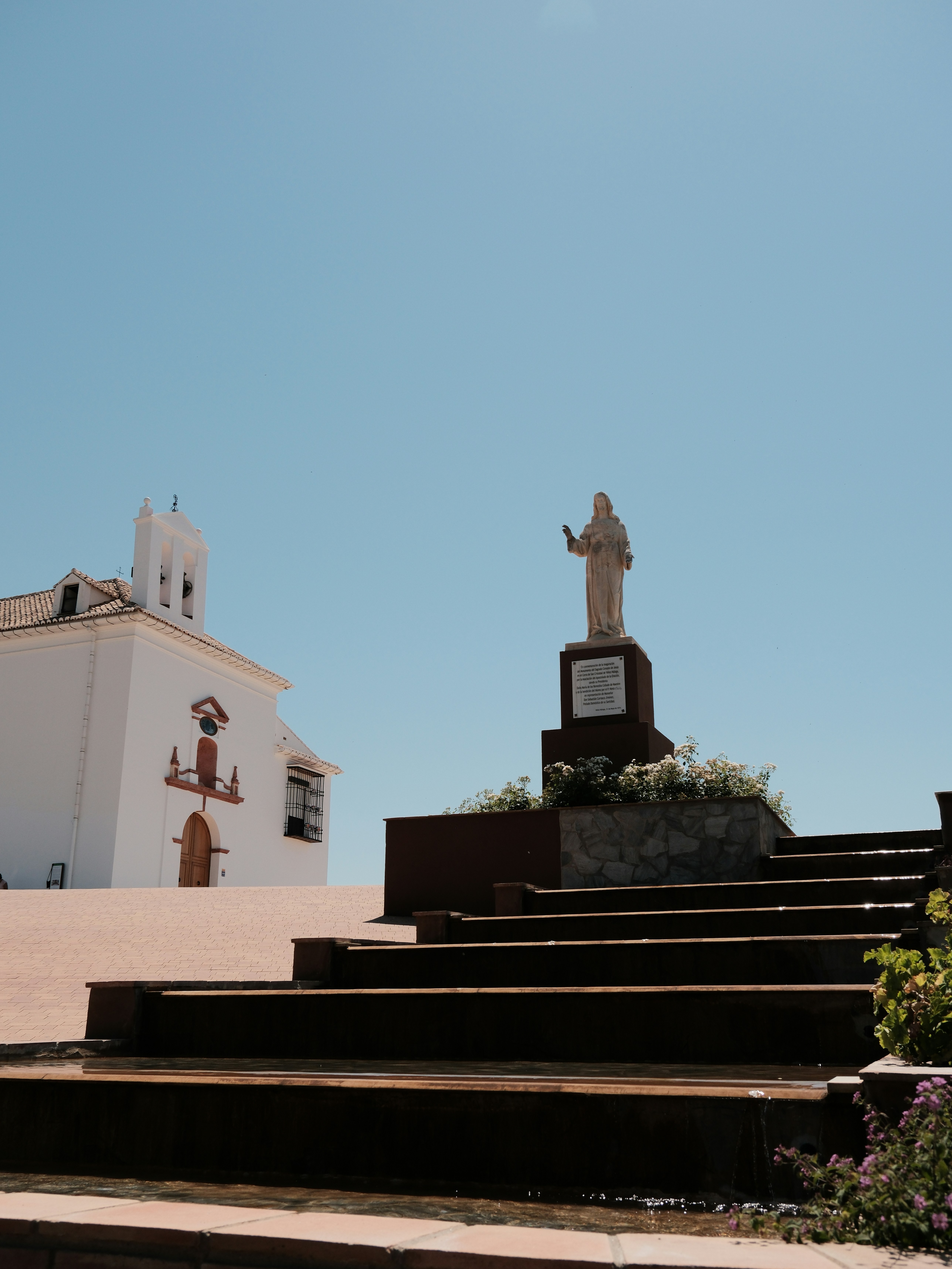Steps toward a statue: a sunlit plaza under a clear blue sky