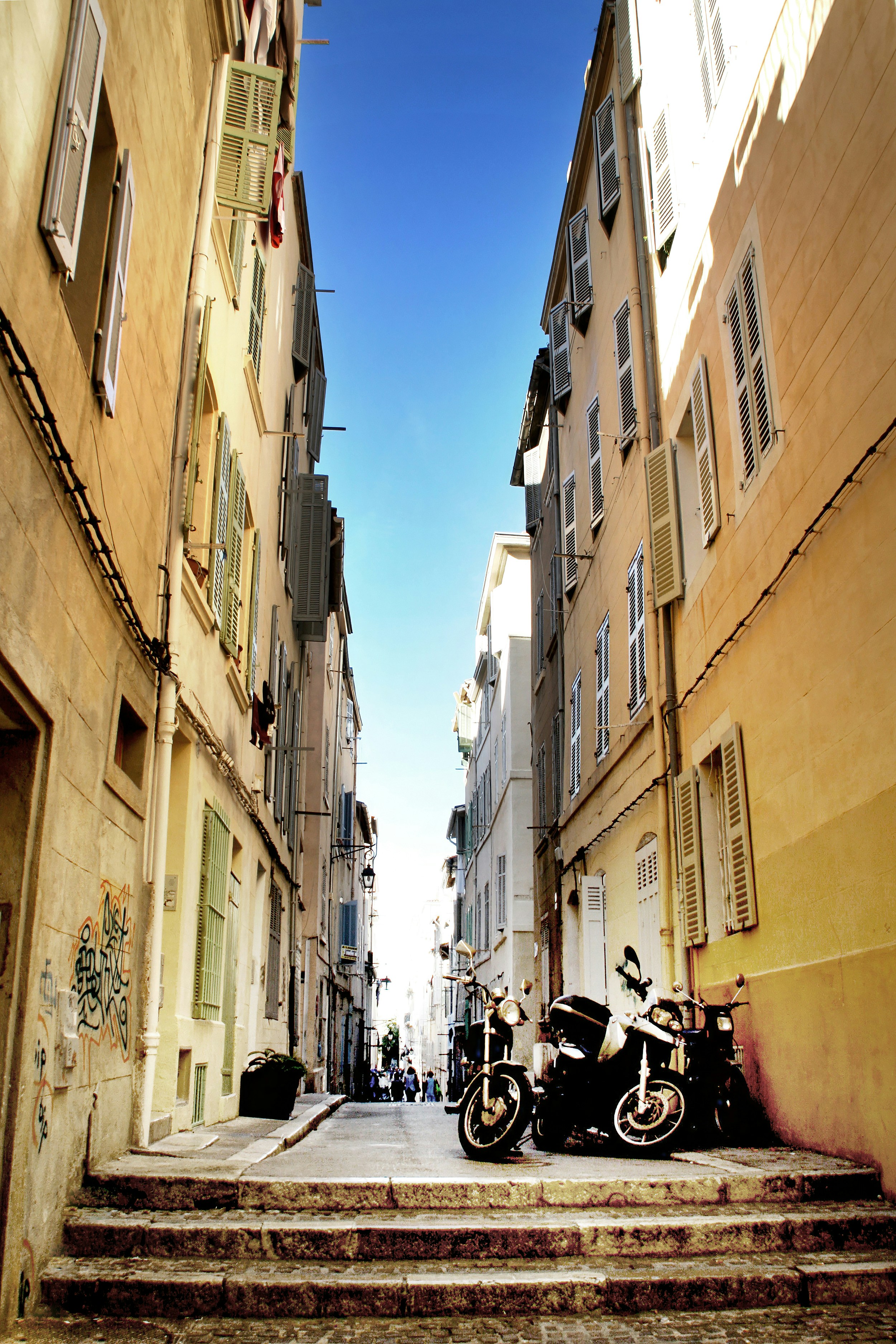 Sunlit Alleyway Ascent: Cars and Steps Between Historic Facades