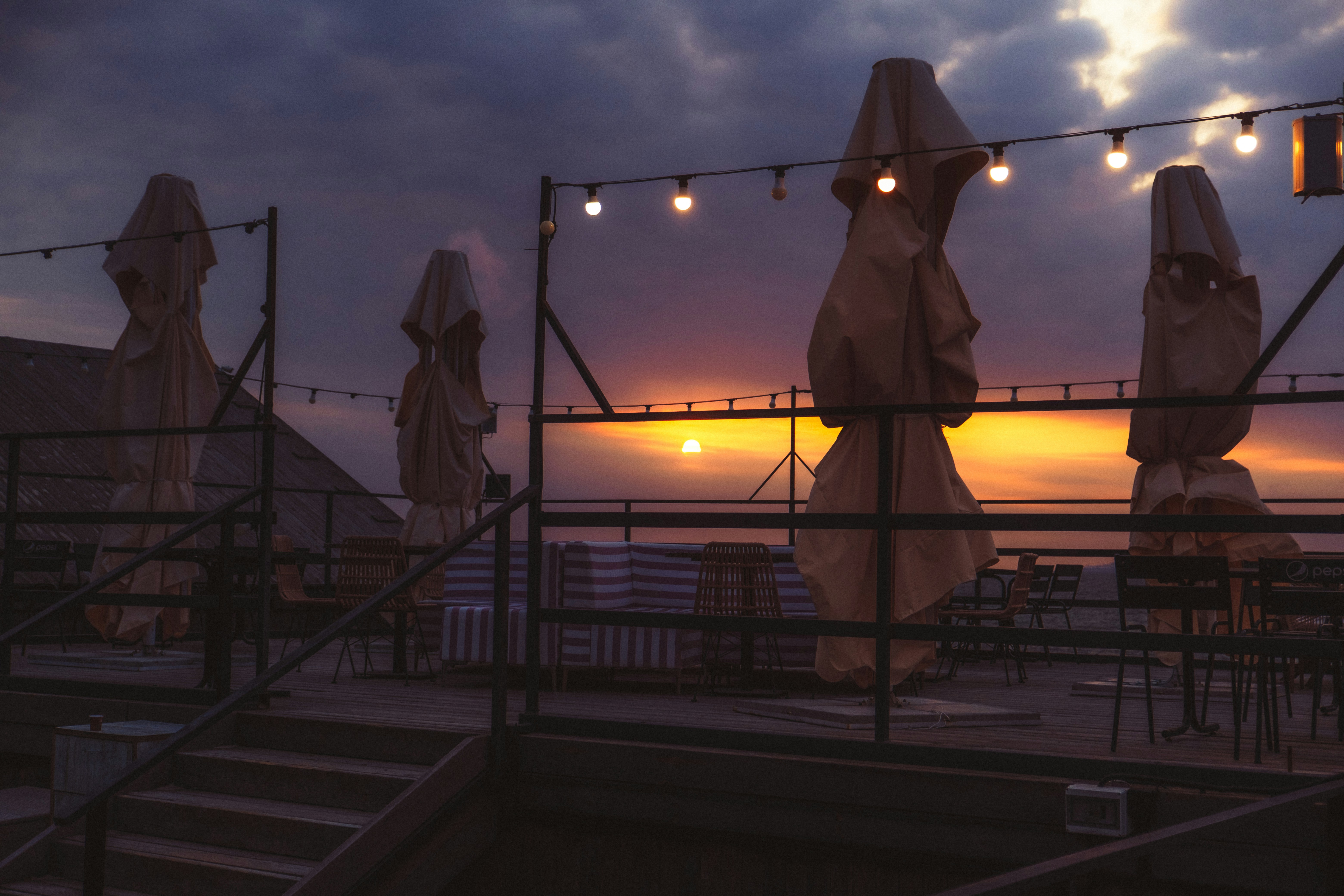 Sunset Rooftop: String Lights and Folded Umbrellas Silhouetted Against a Fiery Horizon