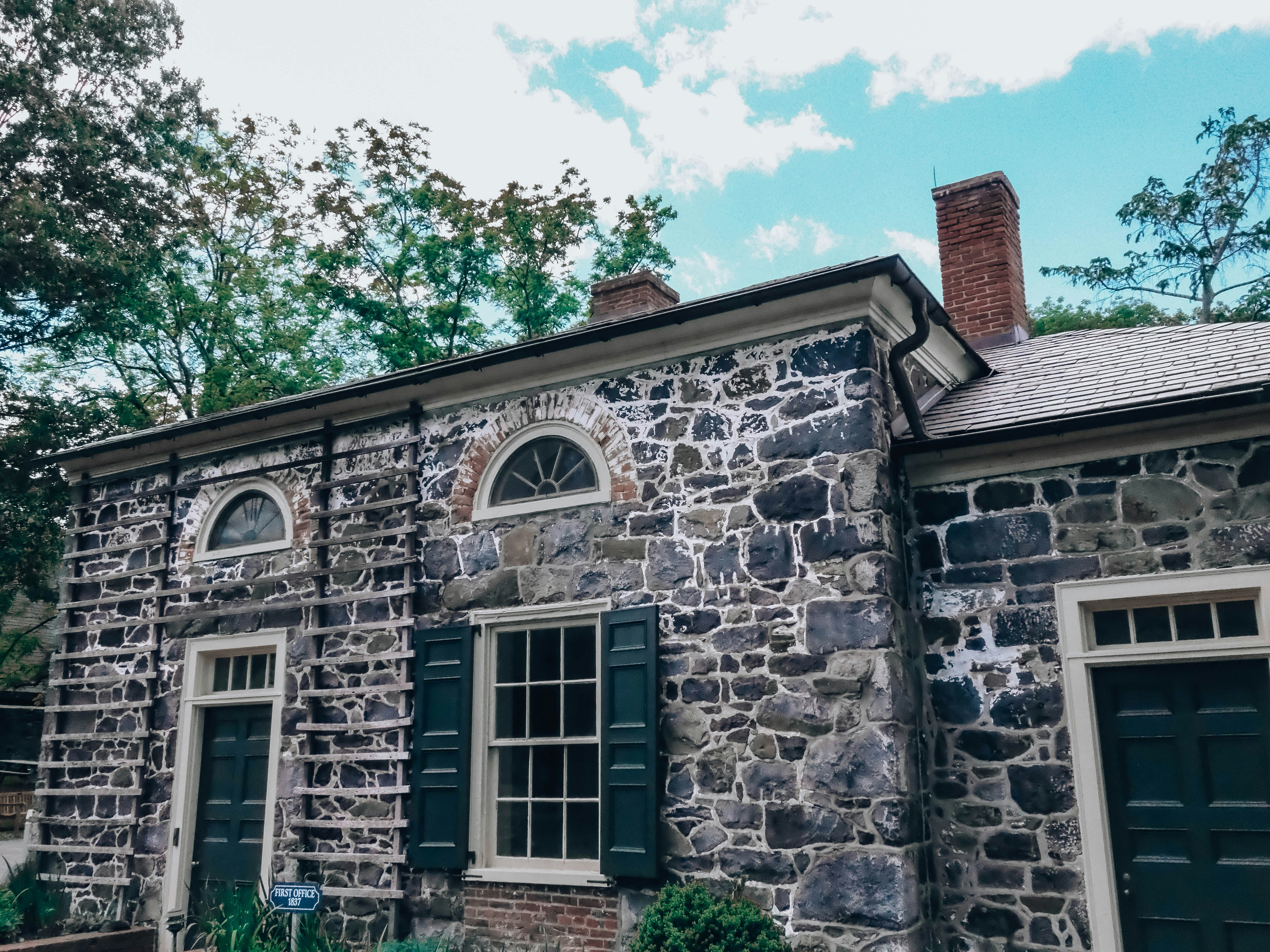 An old stone building with green shutters and a chimney.