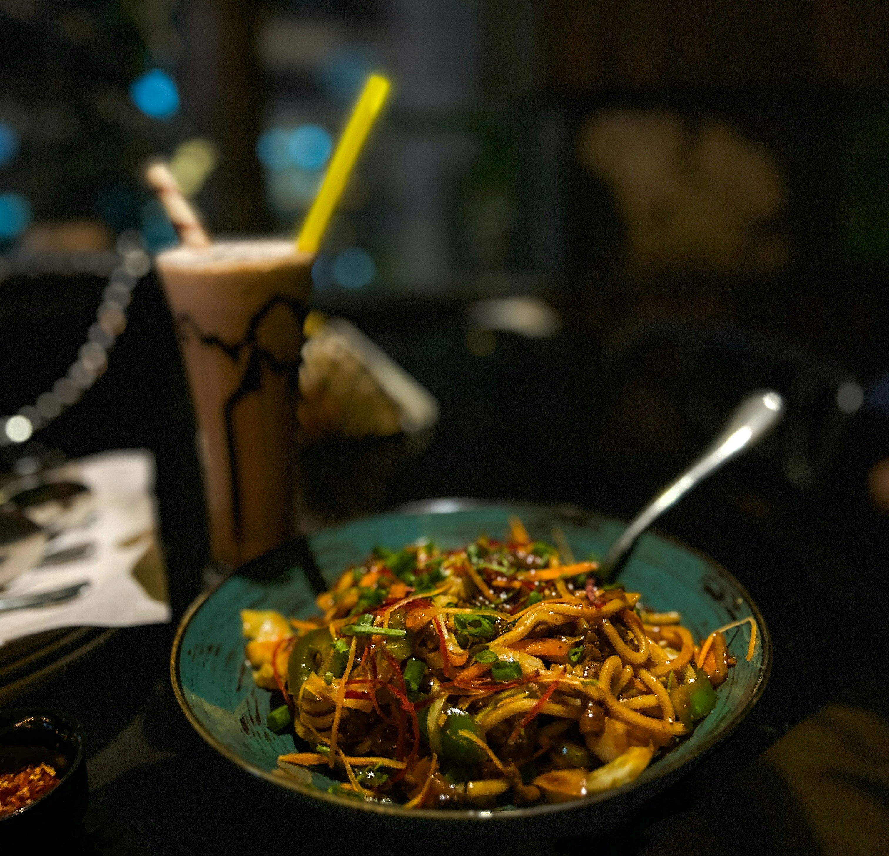 A bowl of stir-fried noodles and a chocolate milkshake.