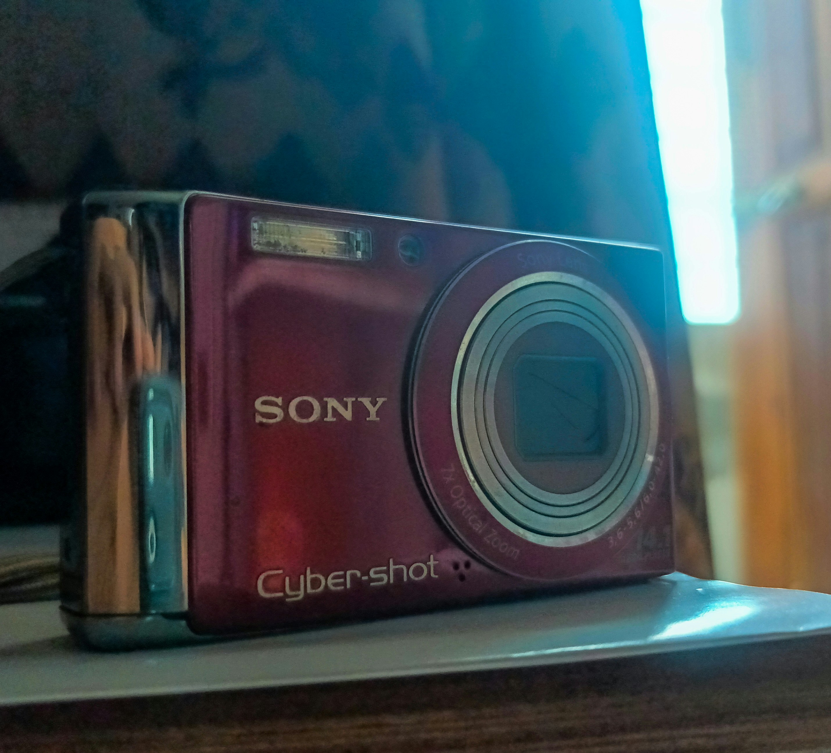Shiny red Sony Cyber-shot on a wooden surface under neon glow