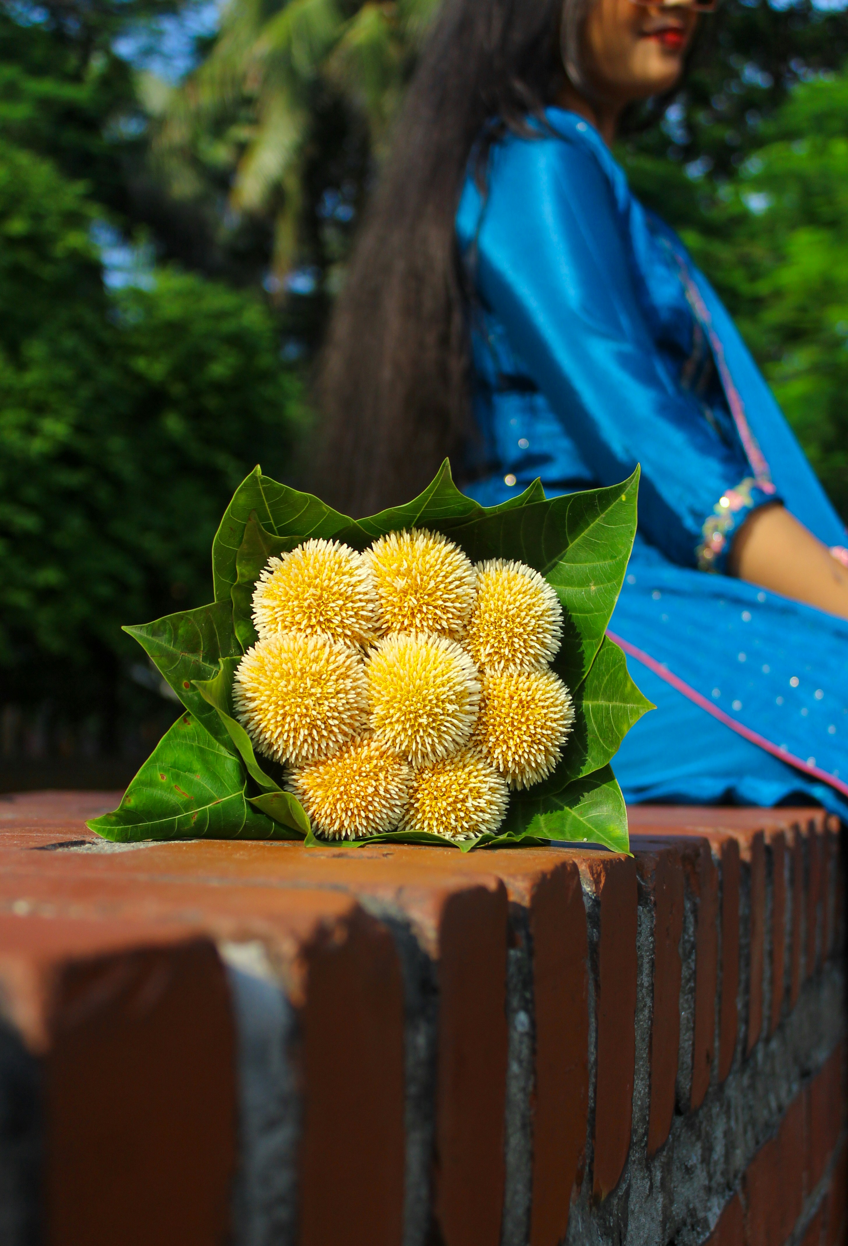 Bright bouquet on a sunlit brick ledge with a blurred blue-clad figure in the background