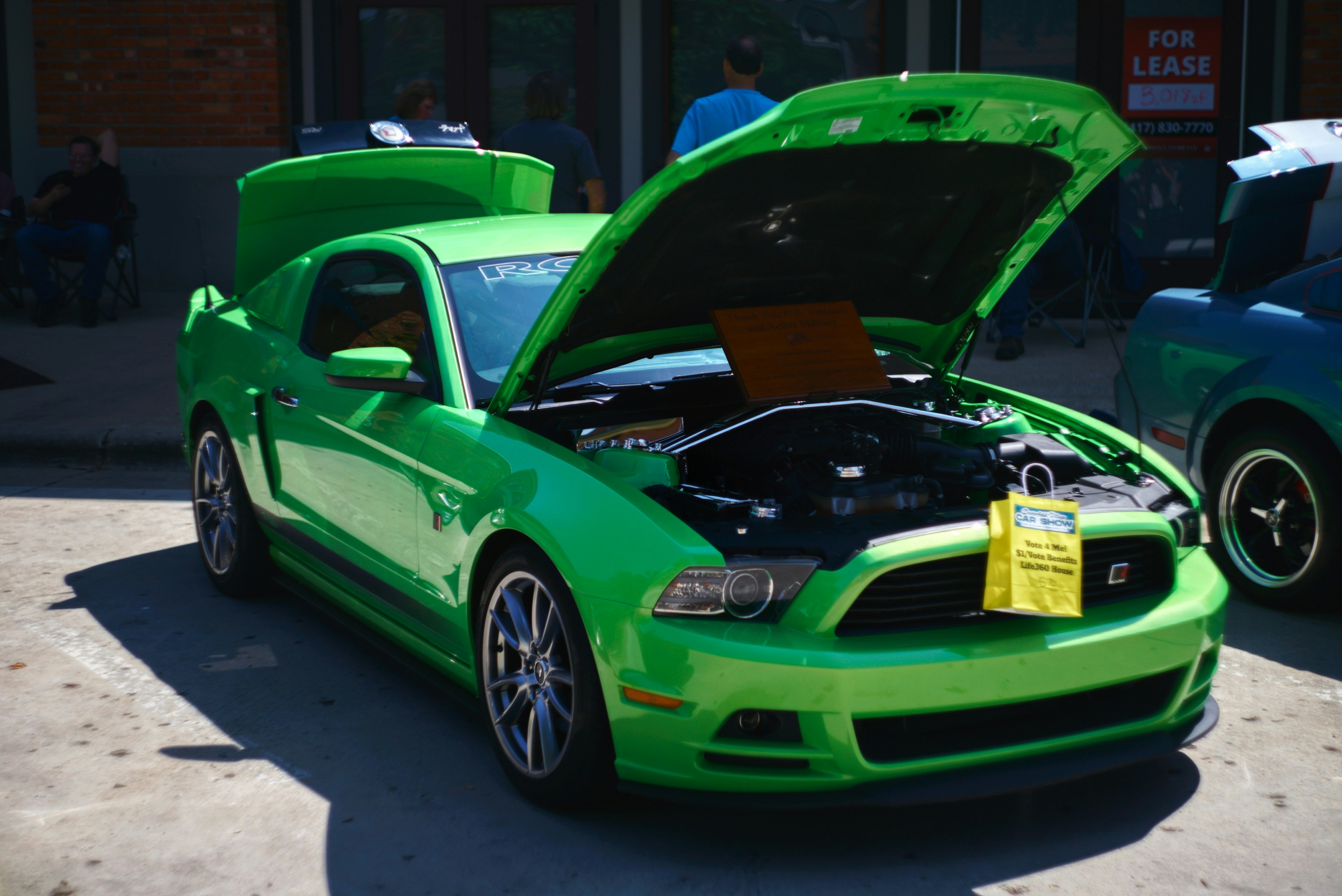 Bright lime-green Ford Mustang with open hood at a car show, engine bay visible under natural light.