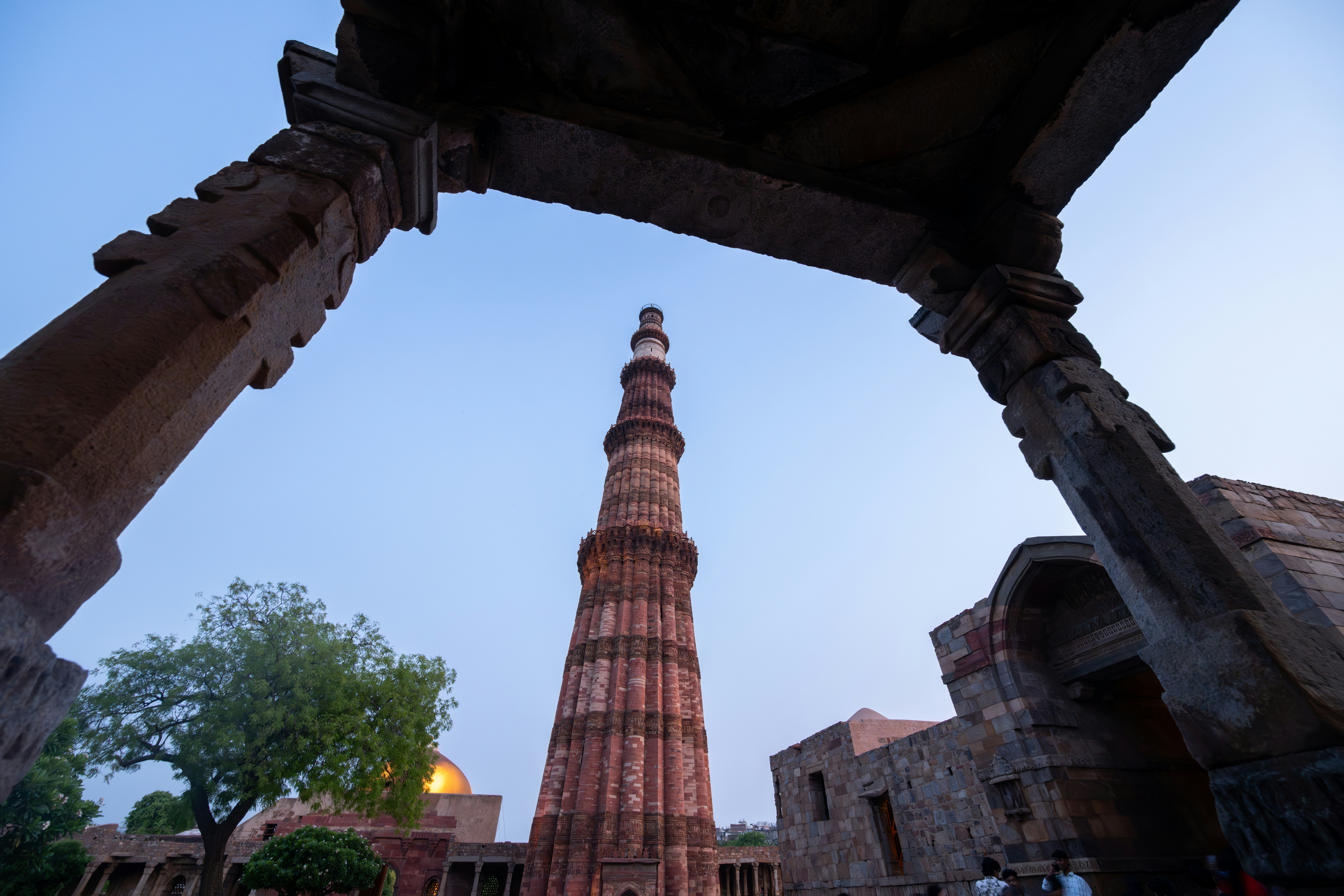 Qutub minar framed by ancient ruins against a clear sky.