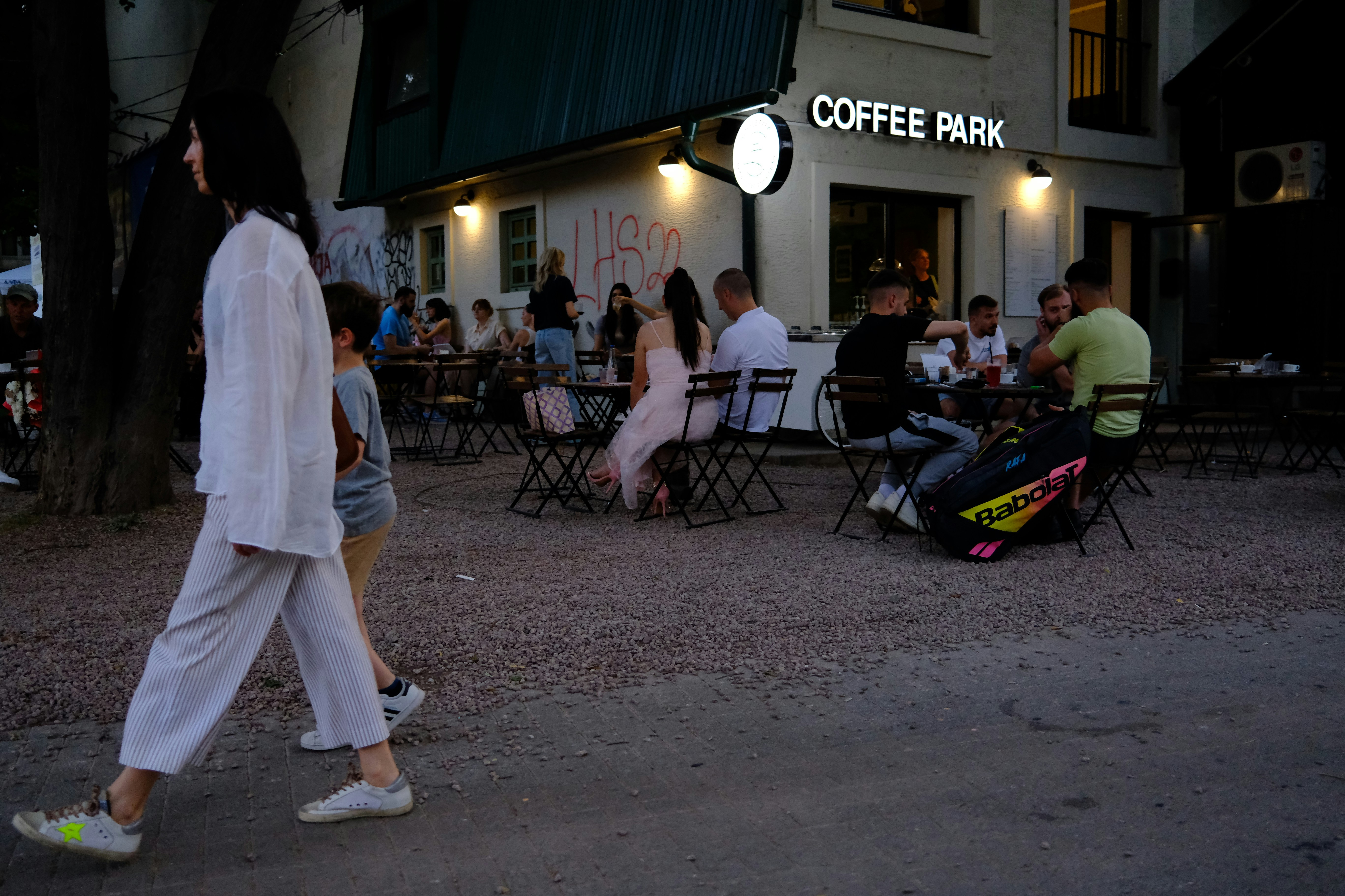 Woman walks past a cafe with people dining outdoors.