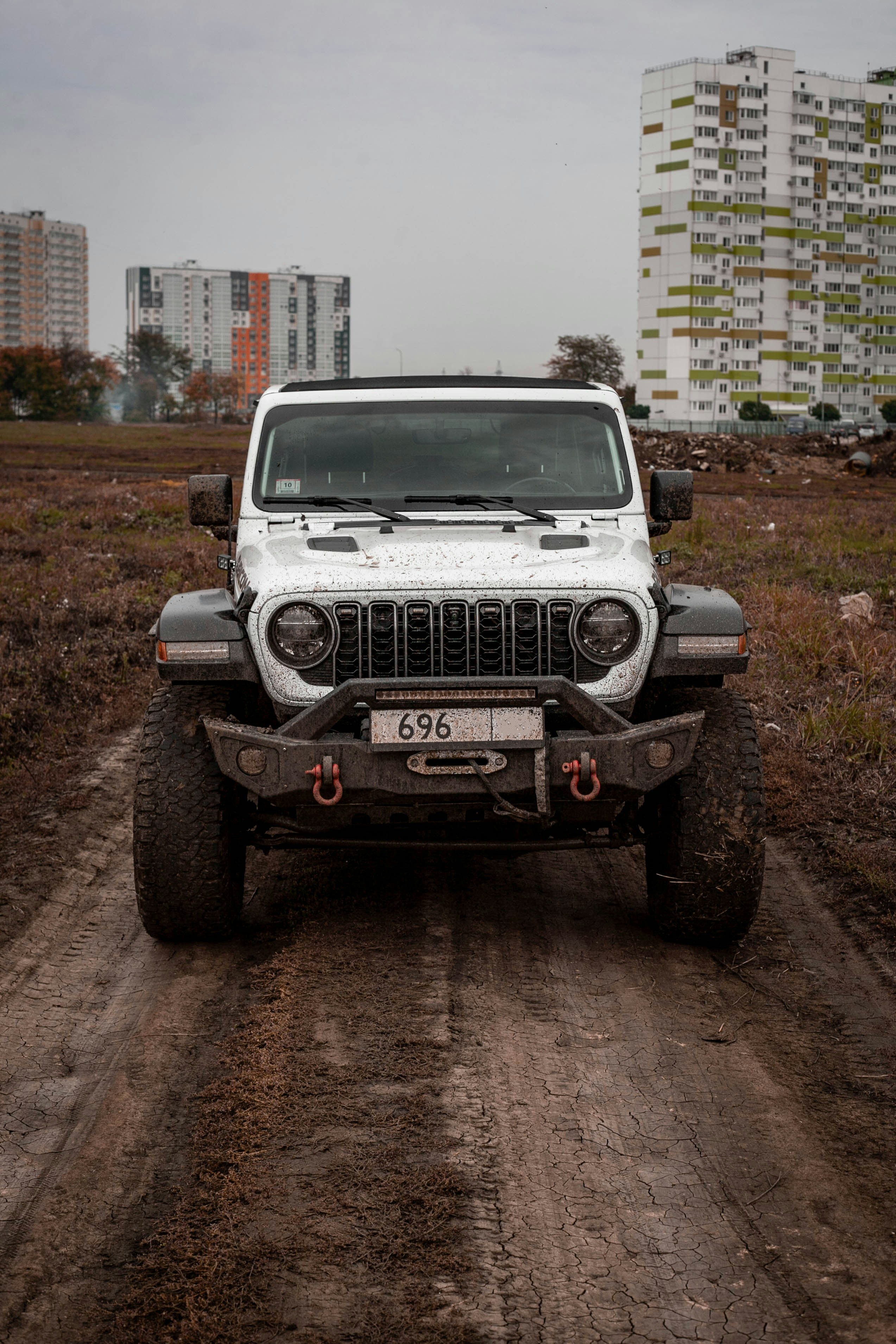 Mud-Crowned Jeep on a Deserted Track Near a Rising Apartment Corridor